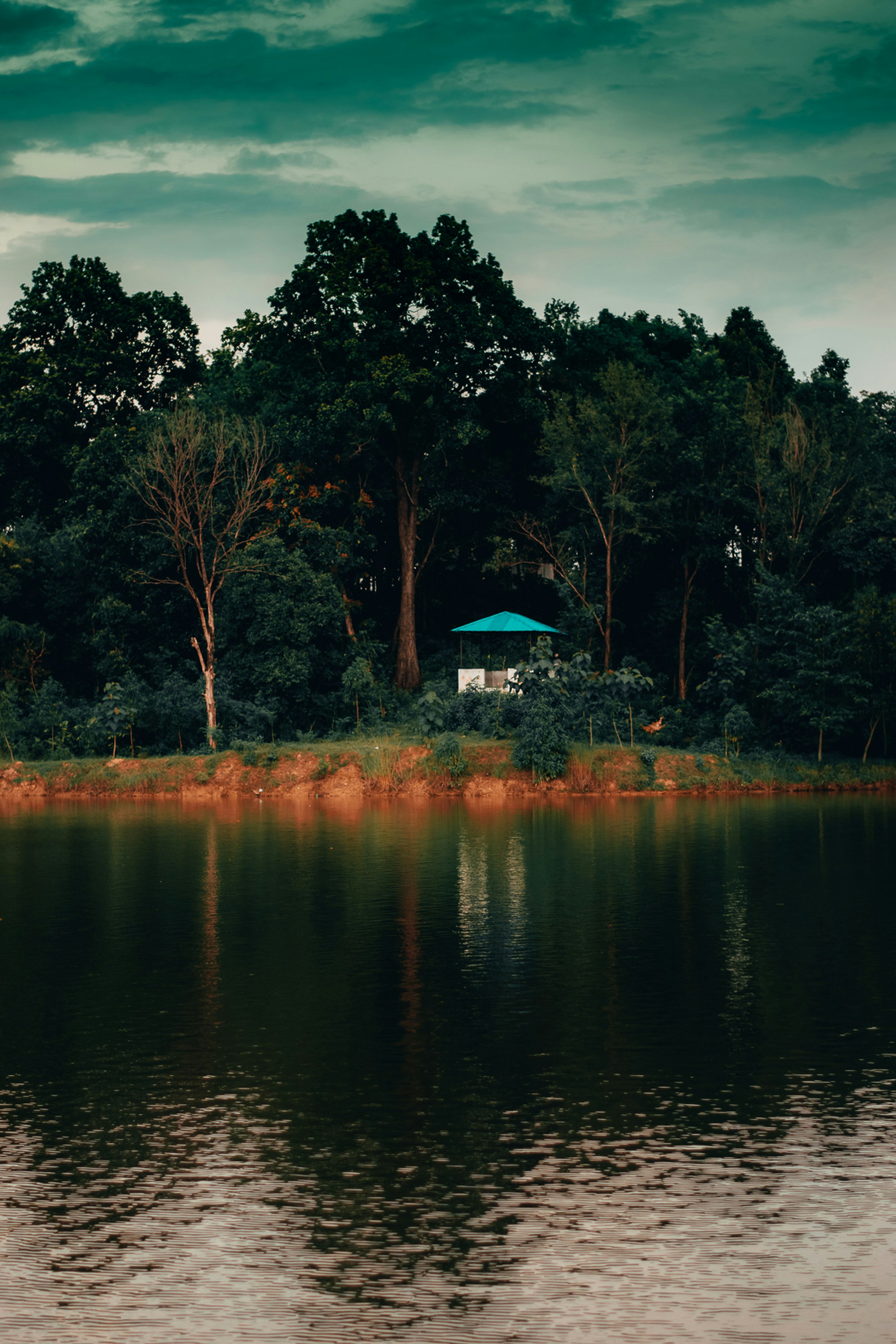 A tranquil gazebo nestled among lush trees, reflecting on the still waters of a serene lake.