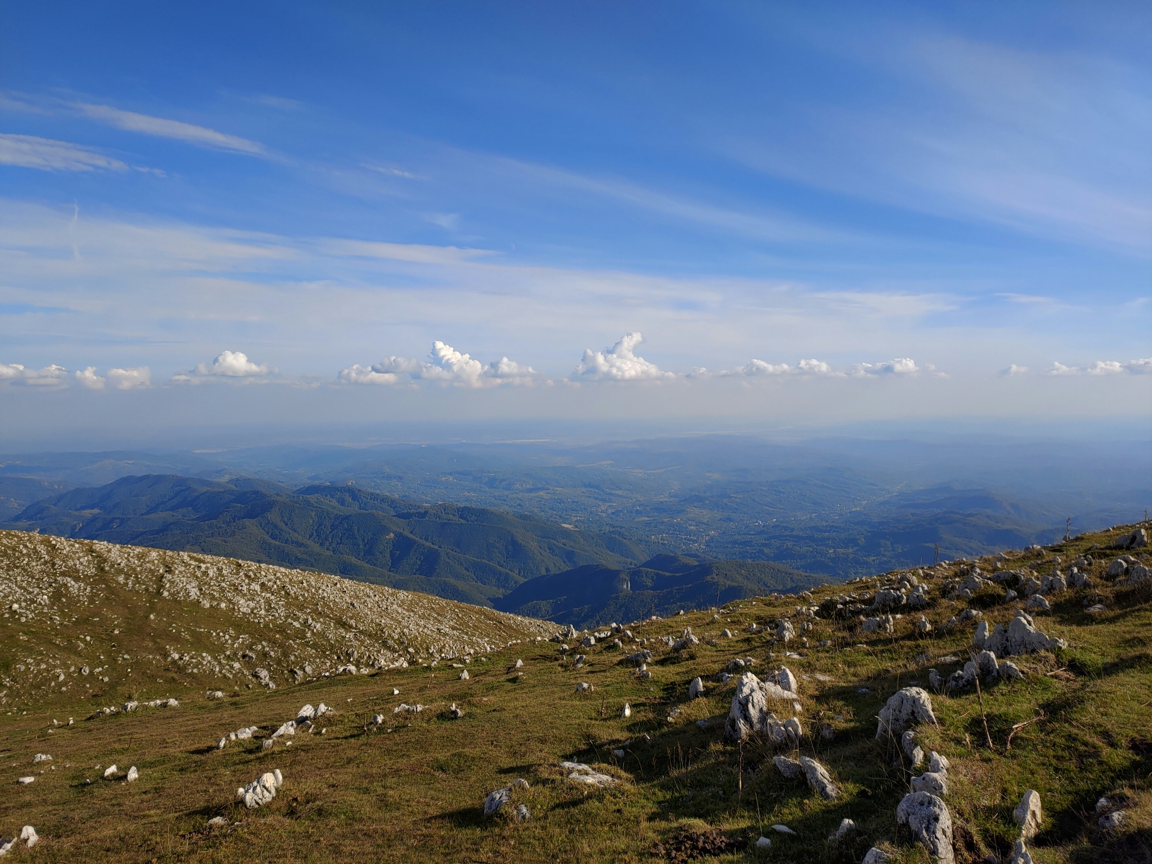 Vast mountain landscape showcasing rolling hills and scattered rocks under a bright blue sky with fluffy clouds. A tranquil scene reflecting nature's beauty.