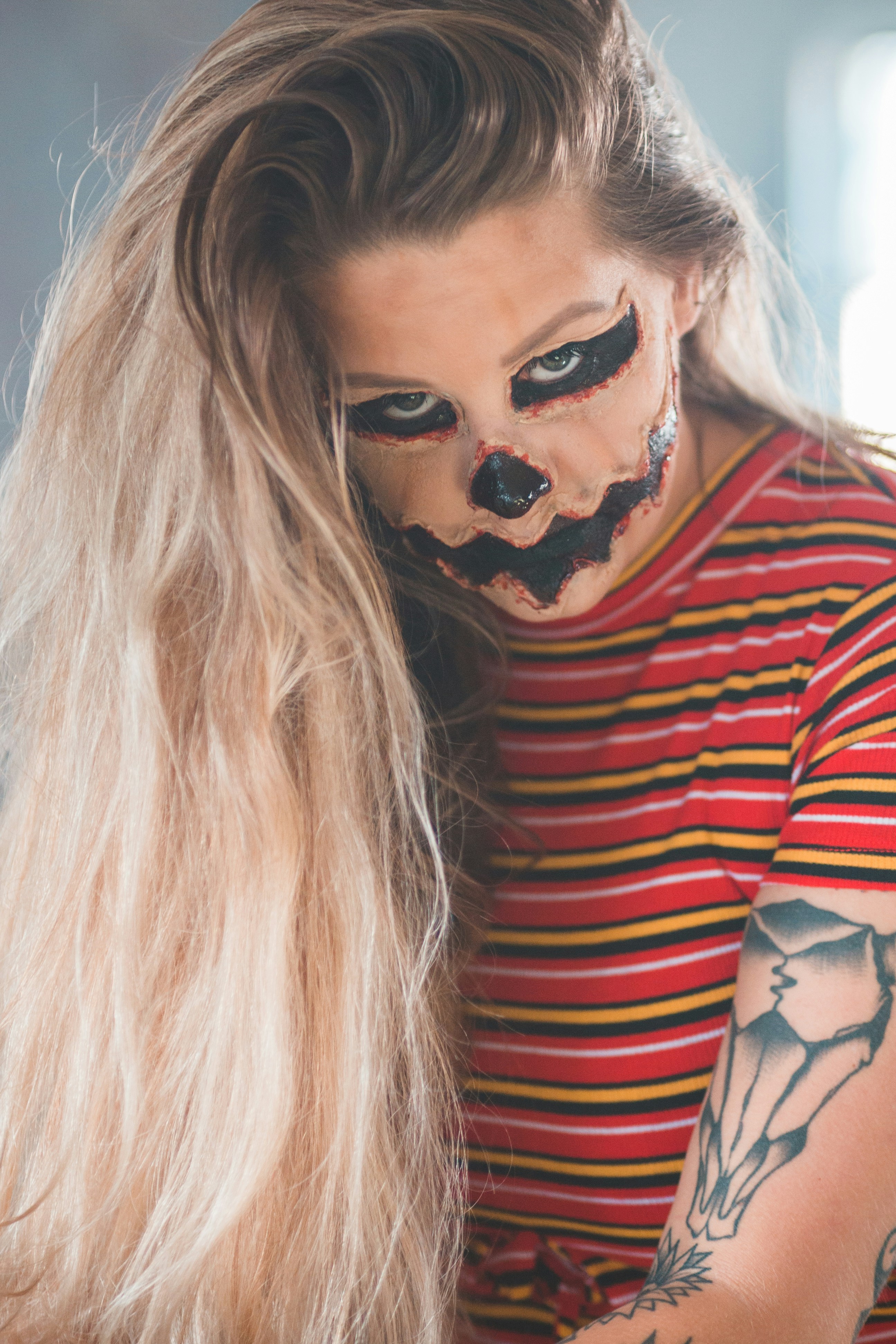 A woman with intricate skull makeup and striking hair poses in a striped top, showcasing a blend of artistry and personality.