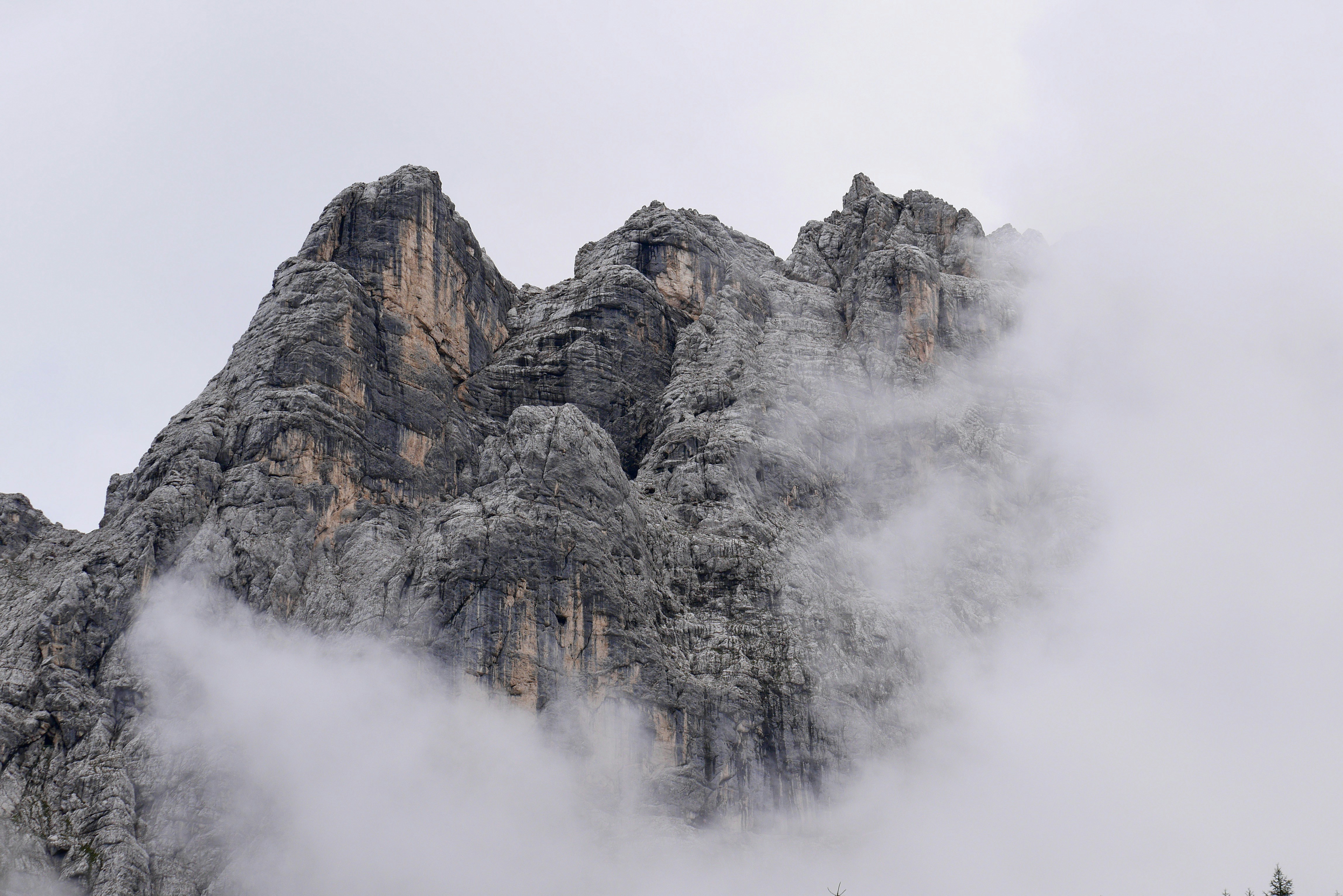 Majestic mountain peaks partially shrouded in mist, revealing rugged textures and dramatic cliffs. The atmosphere evokes a sense of mystery and grandeur.