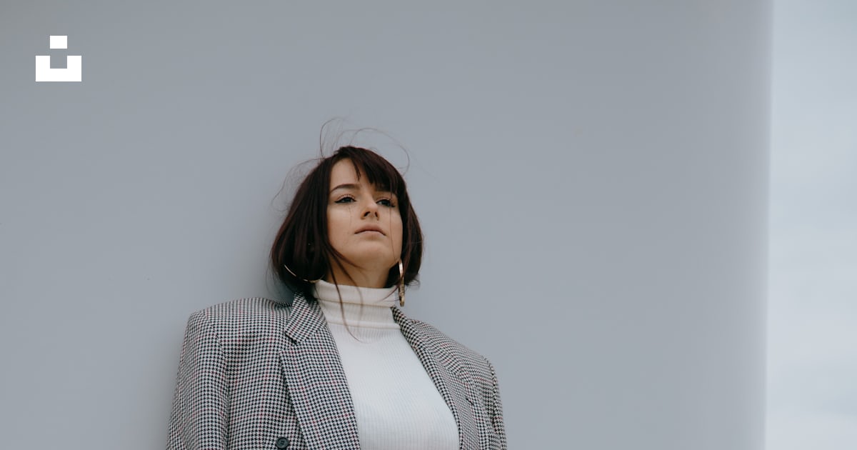 Woman In Gray Coat And Blue Denim Jeans Standing Beside White Wall