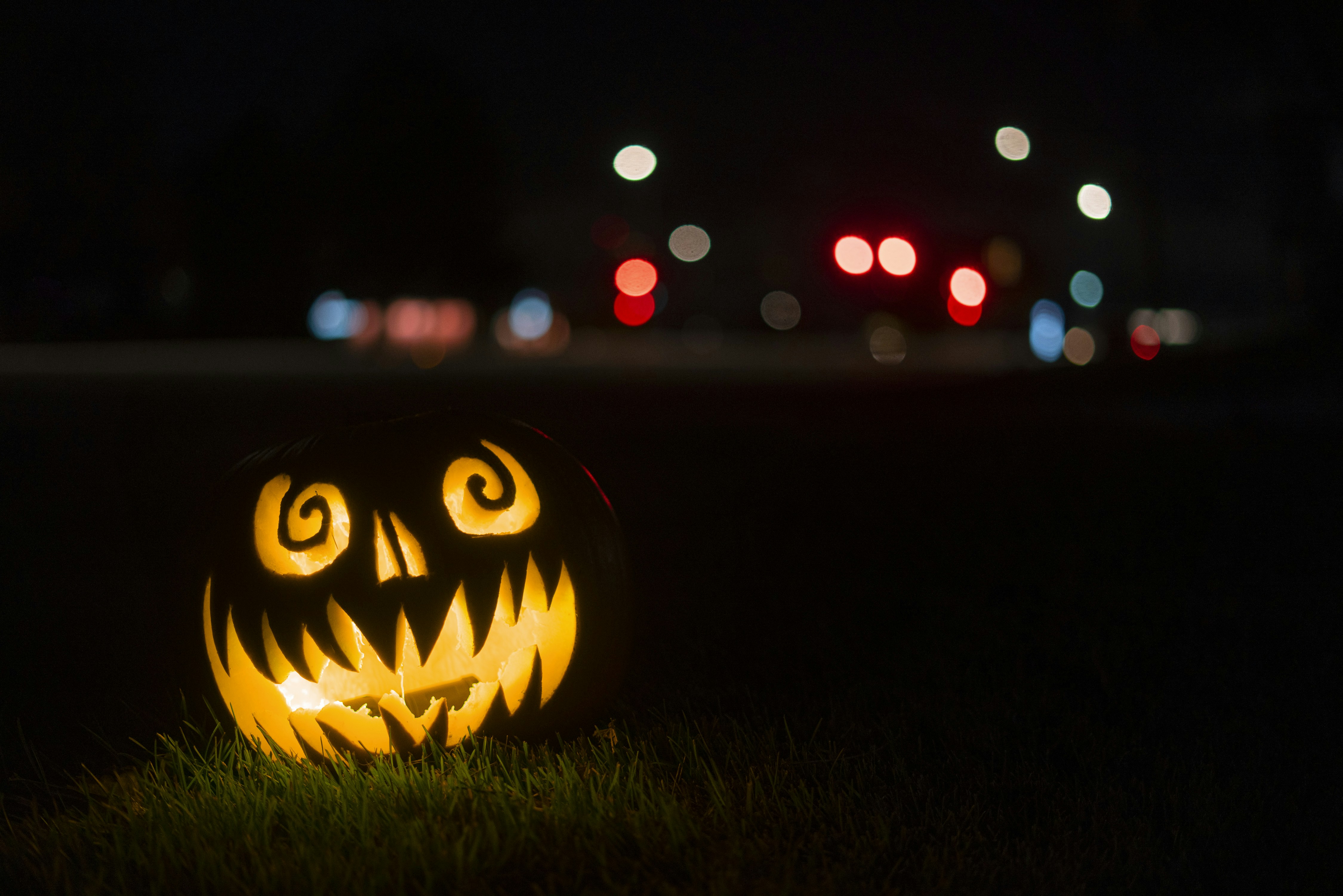 Jack-o'-lantern with spiral eyes and jagged mouth lit up on green grass at night.