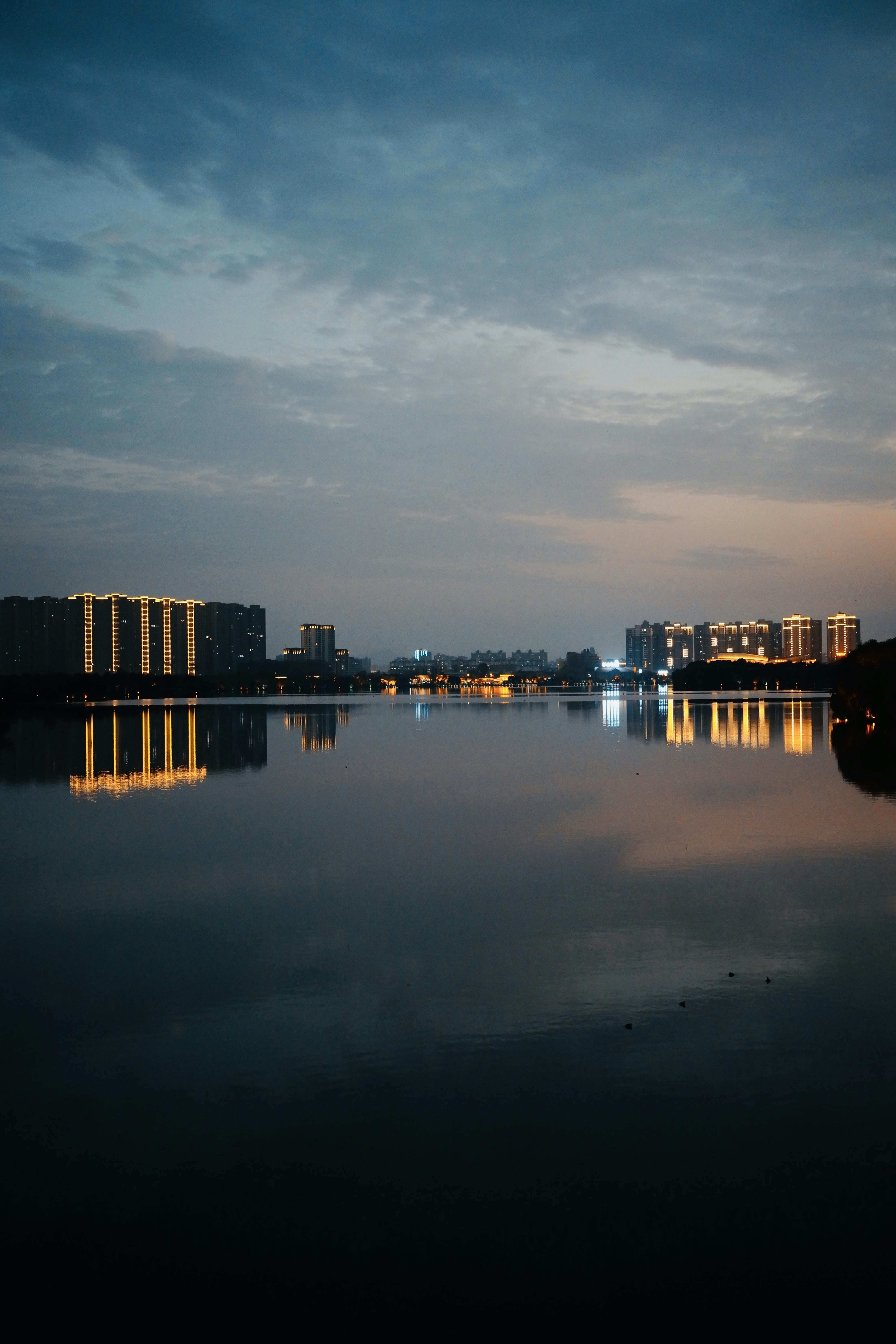 City skyline illuminated at dusk, mirrored in calm water. The scene captures the tranquil beauty of urban life as day transitions to night.