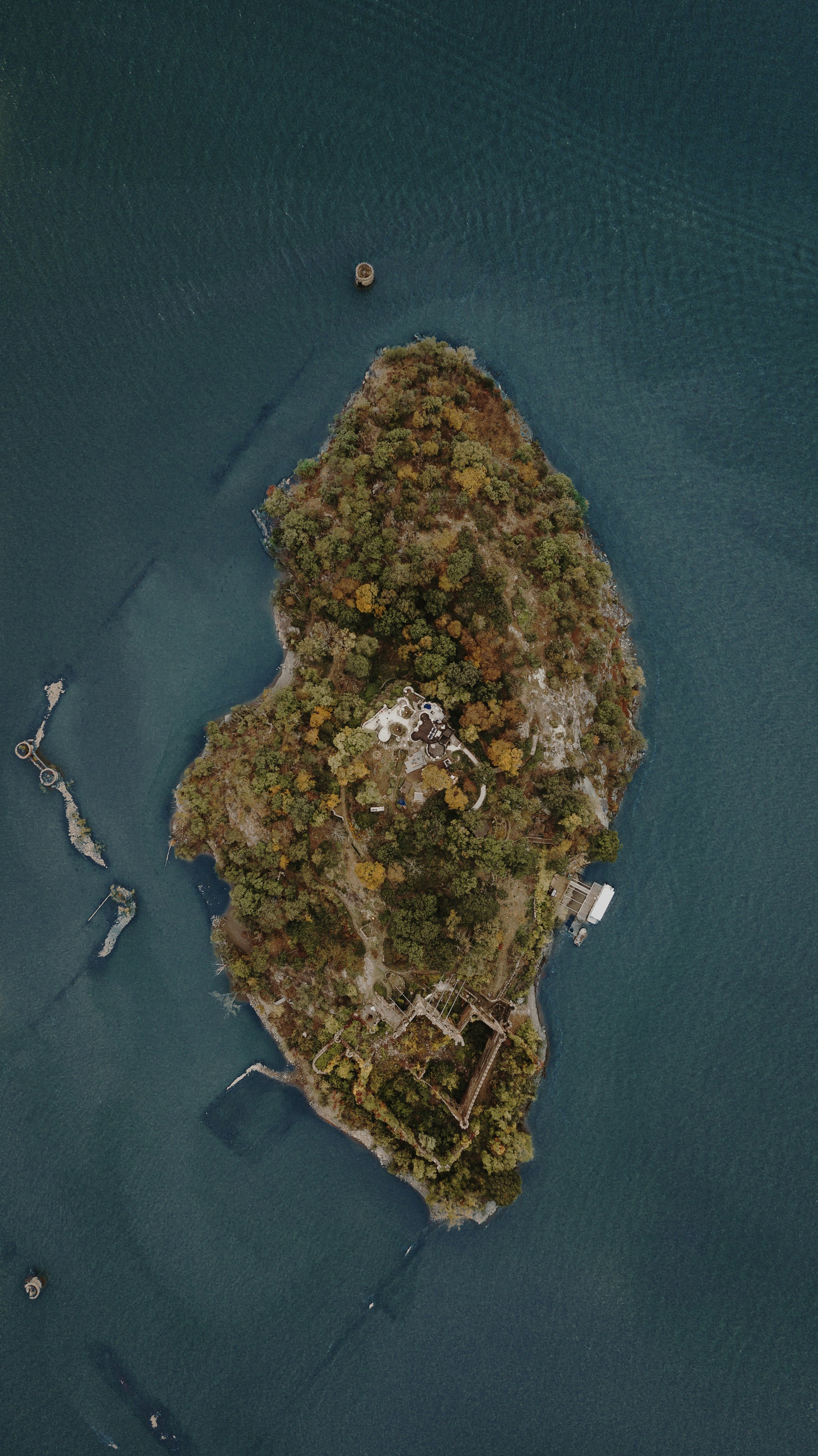 Aerial view of an isolated island showcasing remnants of human activity surrounded by tranquil waters and vibrant autumn foliage.