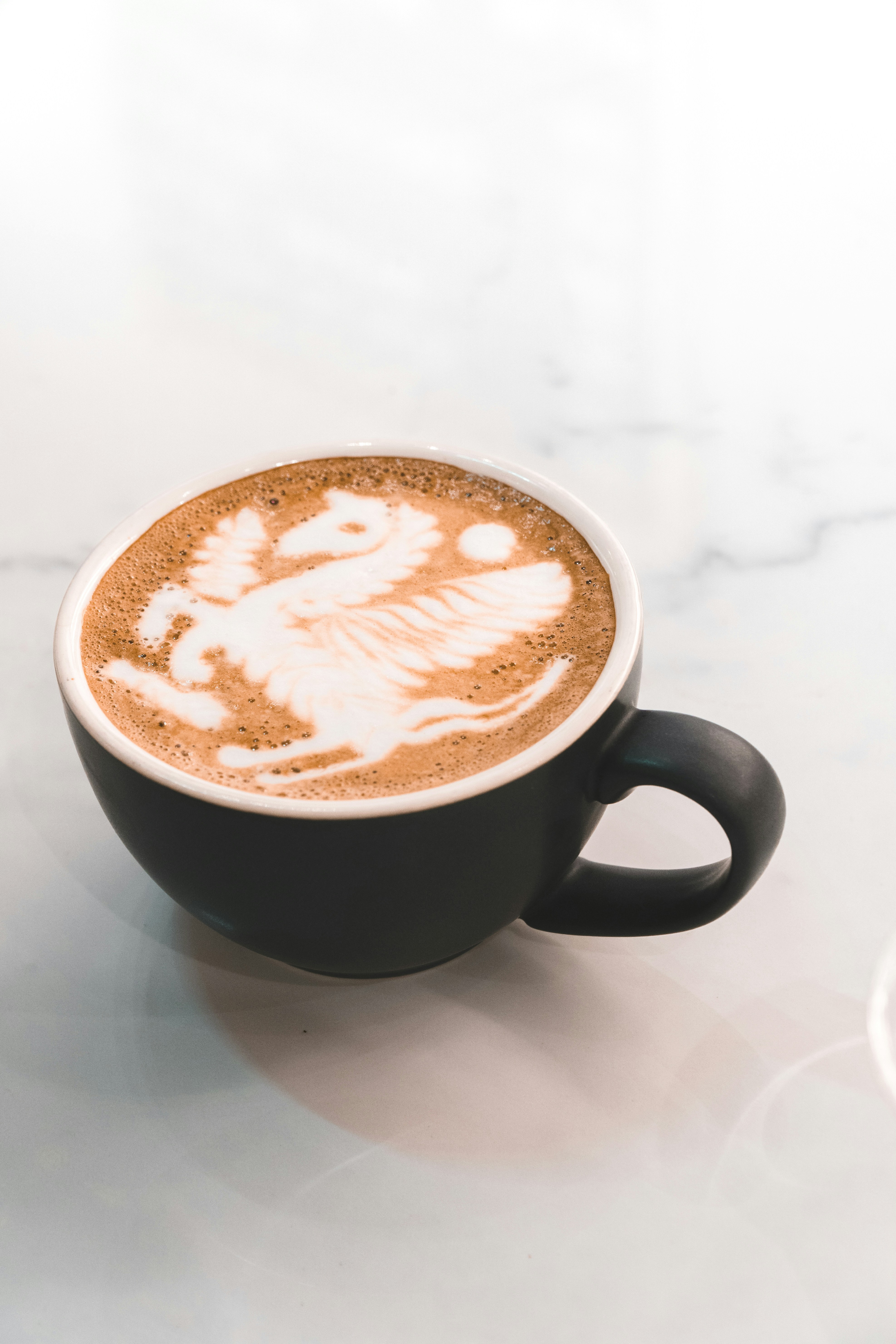Latte art of horse shape from a Barista champion. | black ceramic mug with brown and white heart design