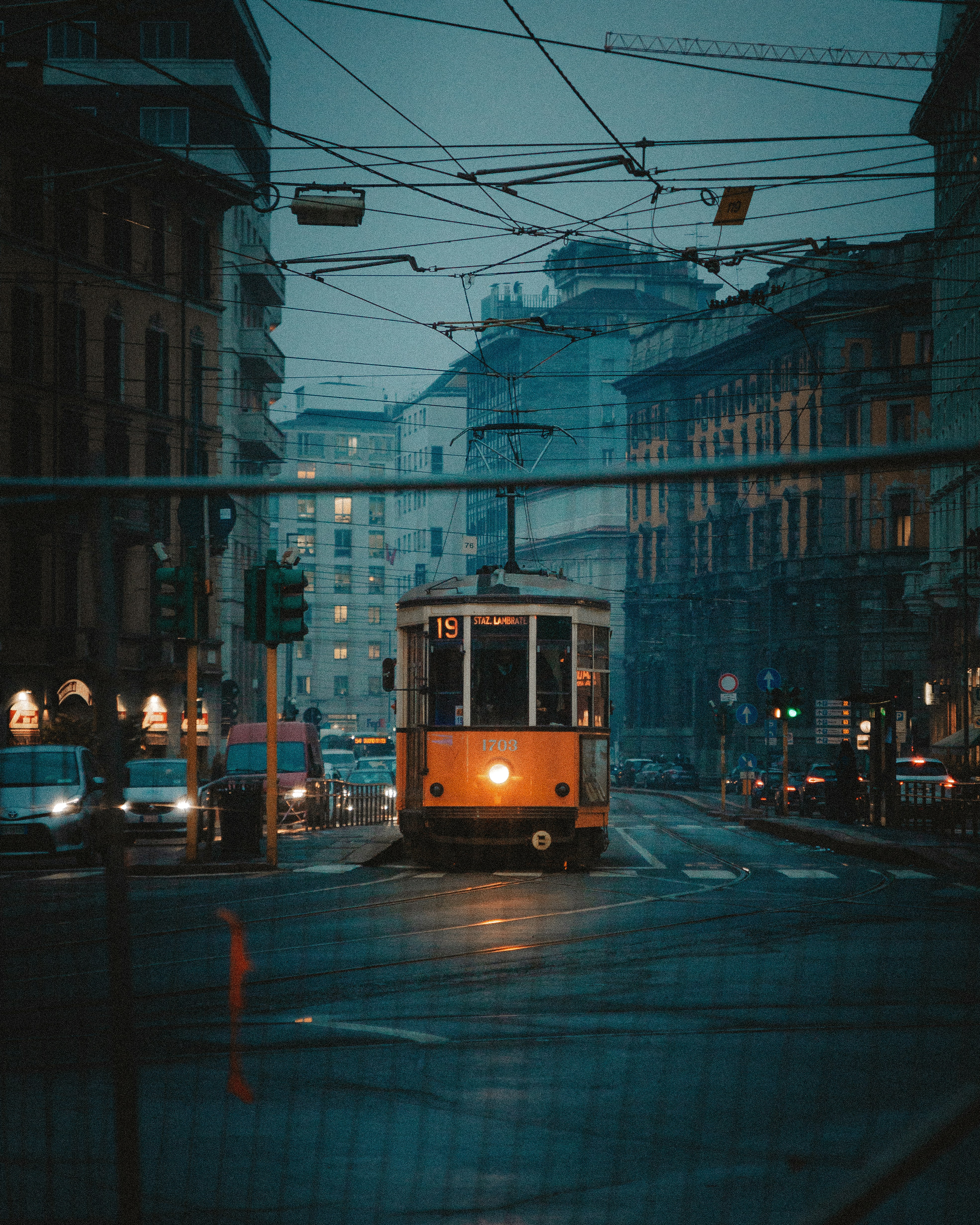 Vintage tram navigating through a bustling city intersection as twilight descends, casting a warm glow amidst the cool blue tones.