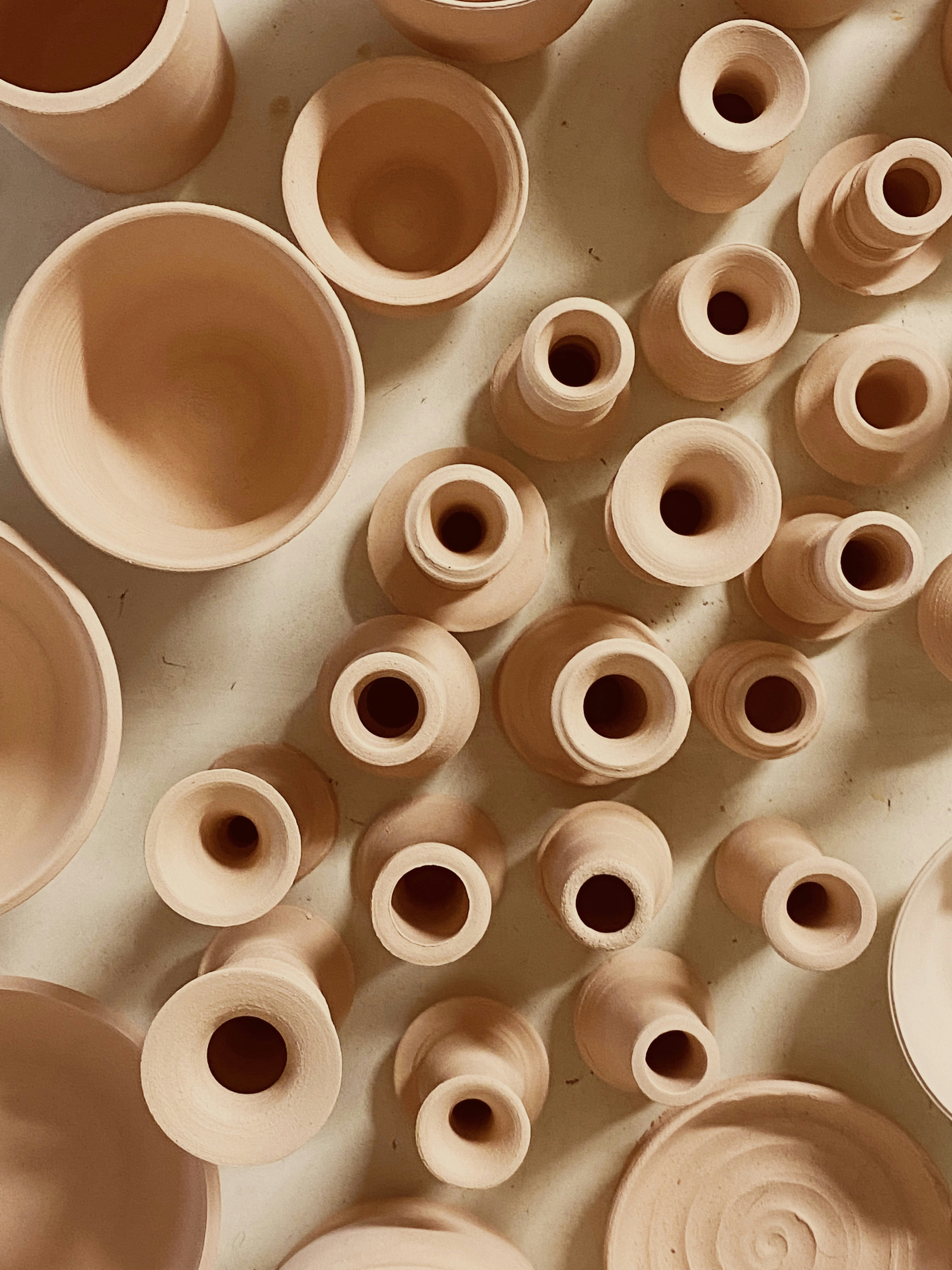 A collection of unglazed clay pots and vessels arranged on a surface, showcasing various shapes and sizes. The natural texture of the clay is highlighted under soft lighting.
