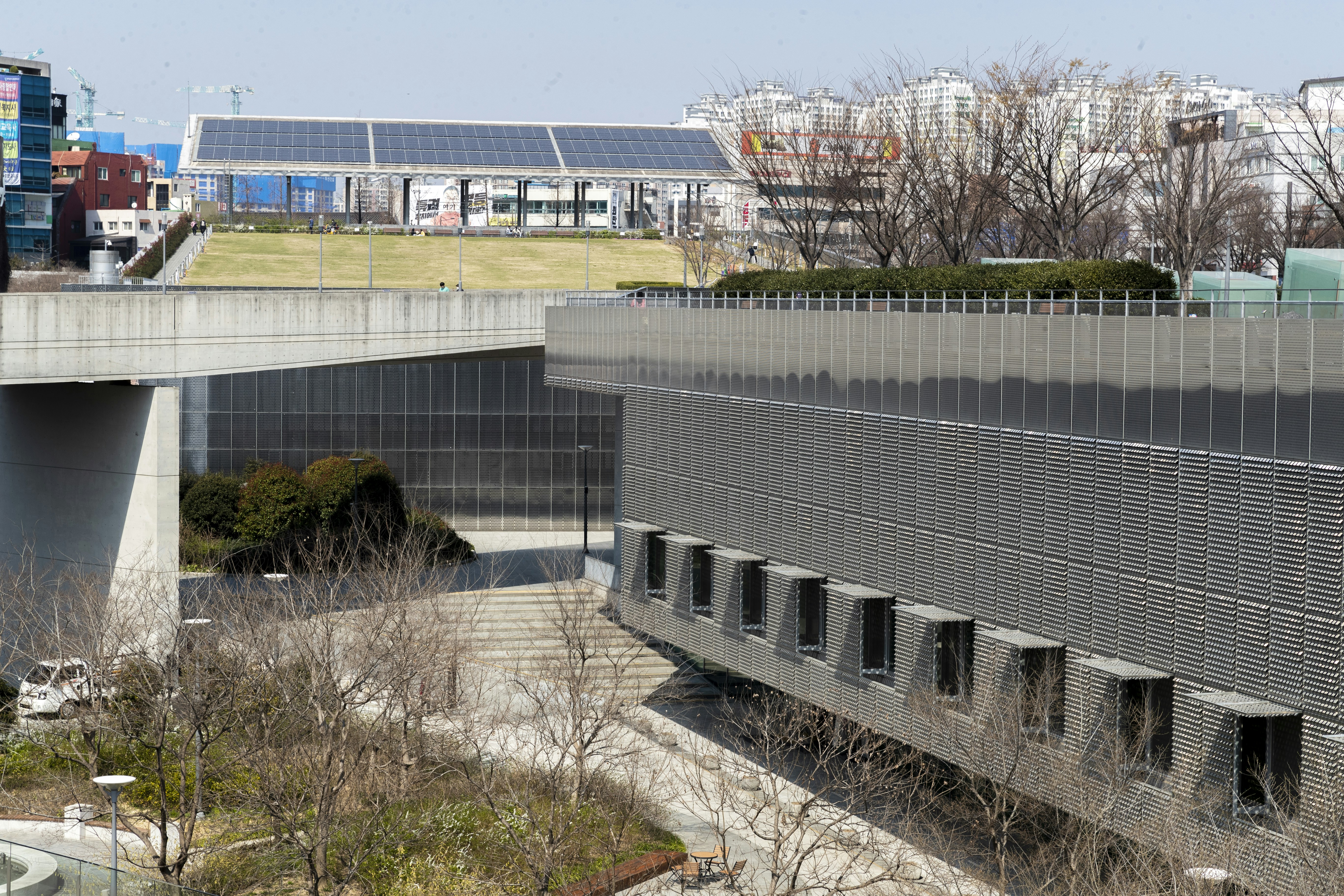 A modern architectural landscape featuring a sleek building juxtaposed with greenery and solar panels in the background.