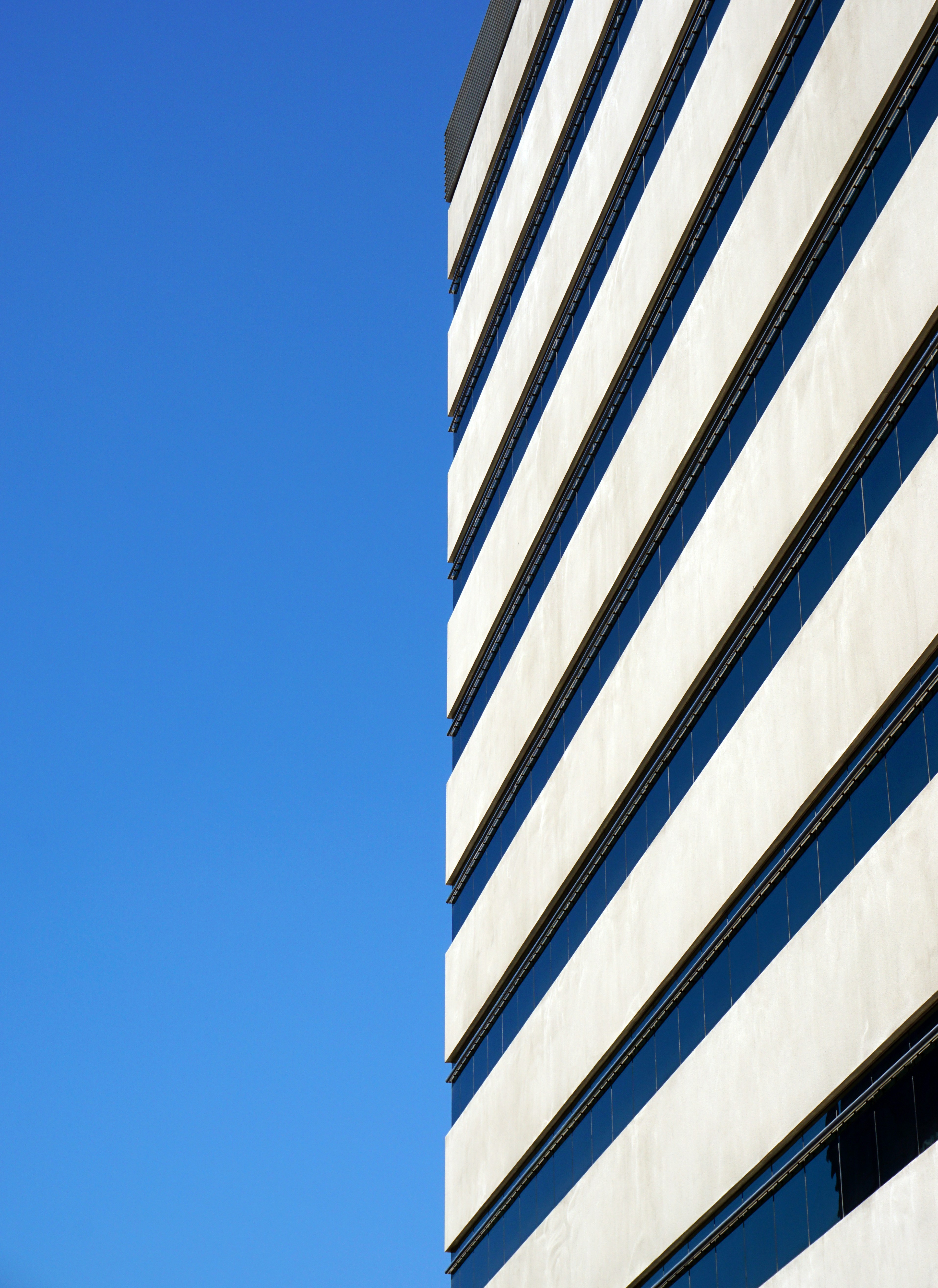 Geometric facade of a contemporary building showcasing alternating stripes of glass and concrete against a clear blue sky.