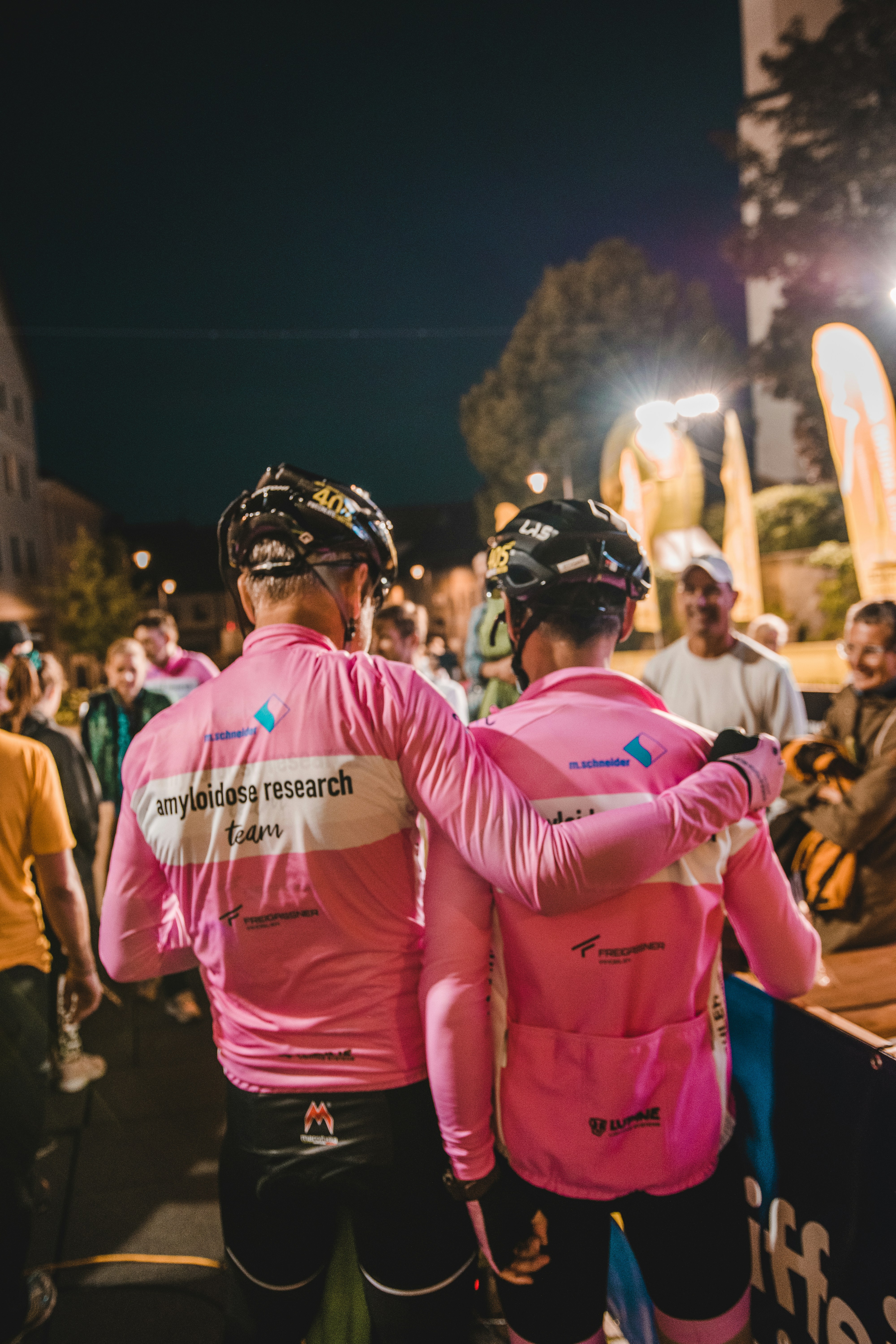 Two Cyclists in Pink Team Jerseys Embrace at Night Rally