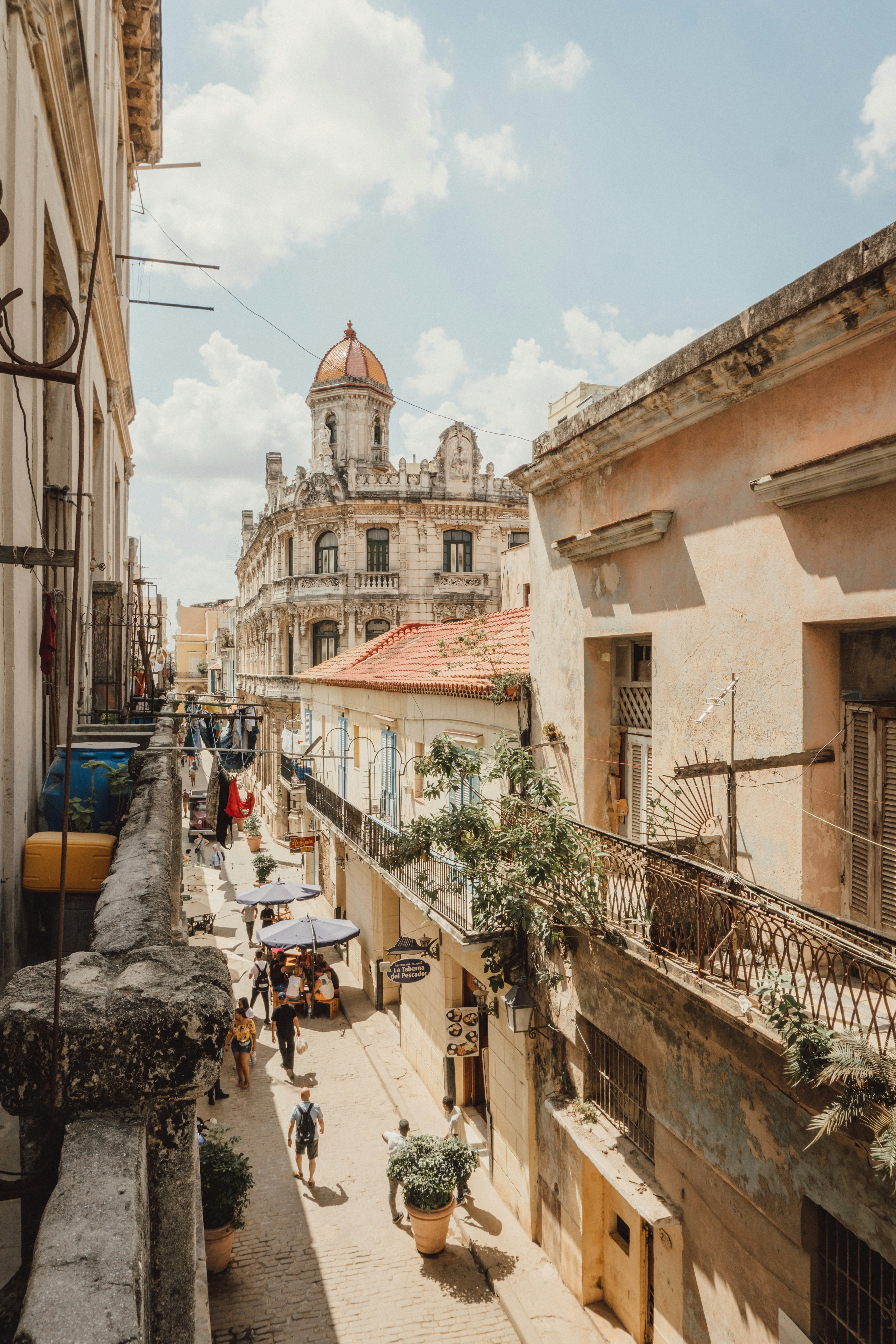 Charming narrow street in Havana lined with historic buildings and lively pedestrians. The ornate architecture and vibrant atmosphere reflect the city's rich cultural heritage.