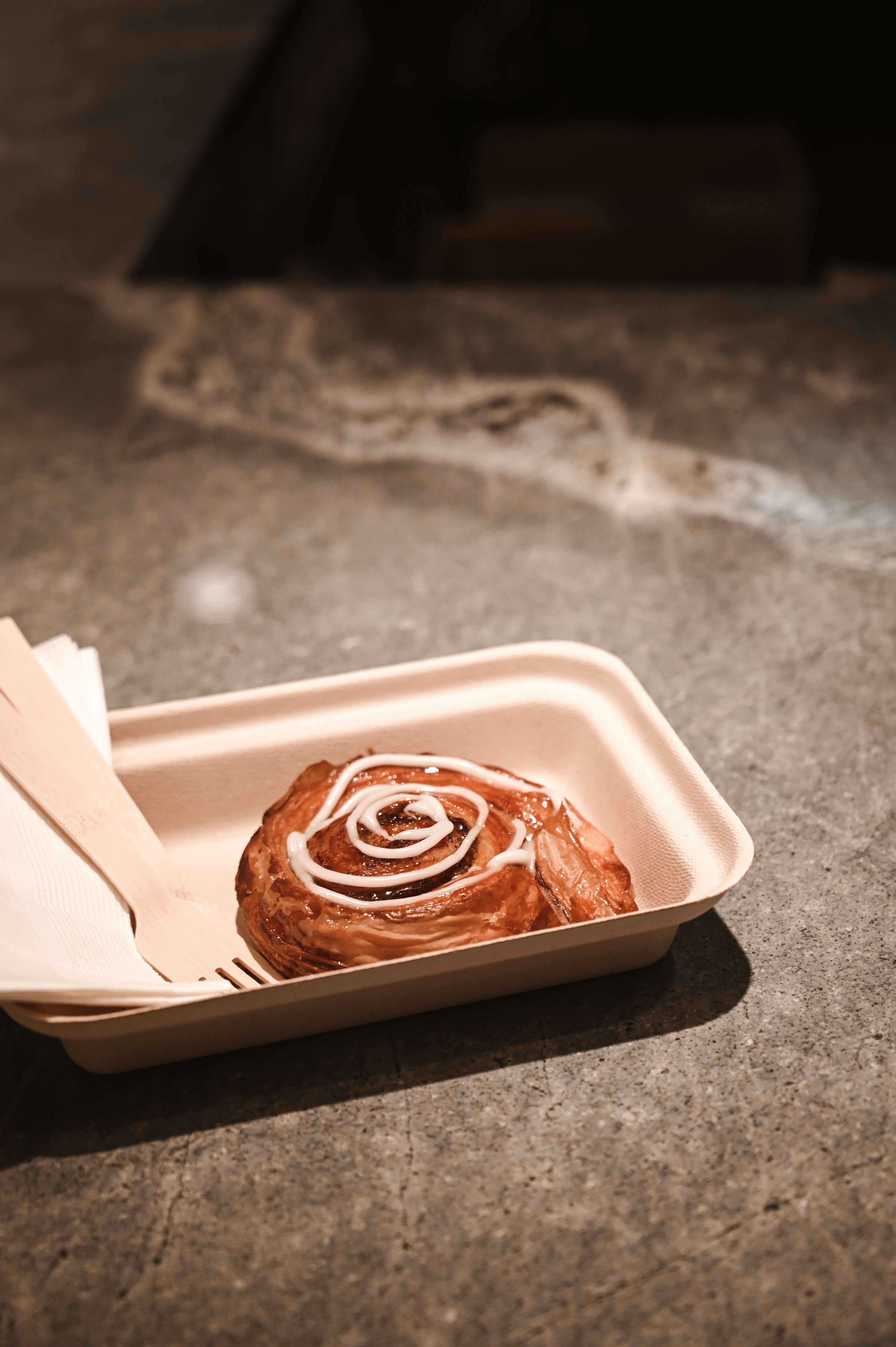Soft-lit Cinnamon Roll in a Takeout Tray: Quiet Breakfast Moment