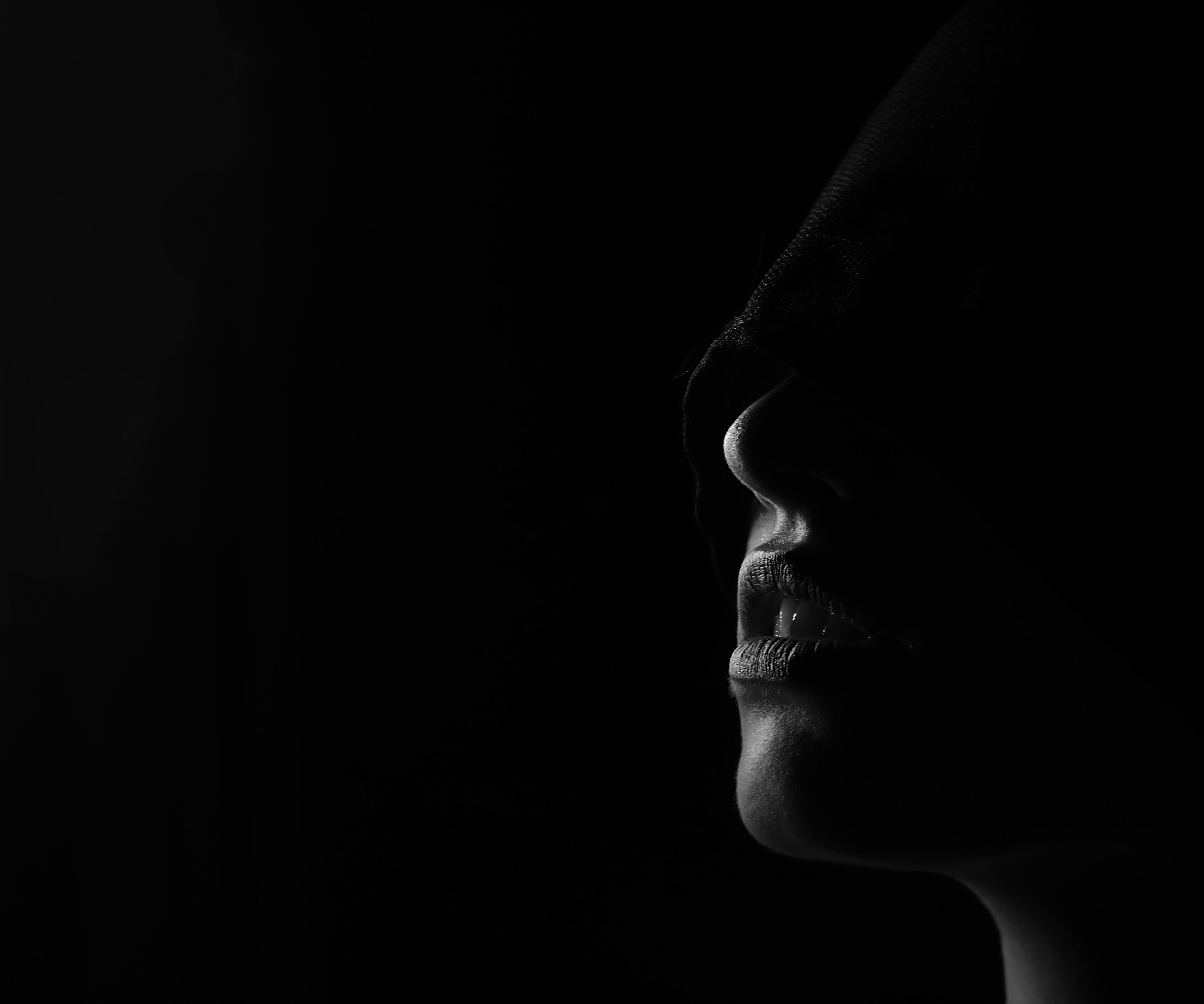 Silhouetted woman's face partially covered in shadow, highlighting textured lips in grayscale.