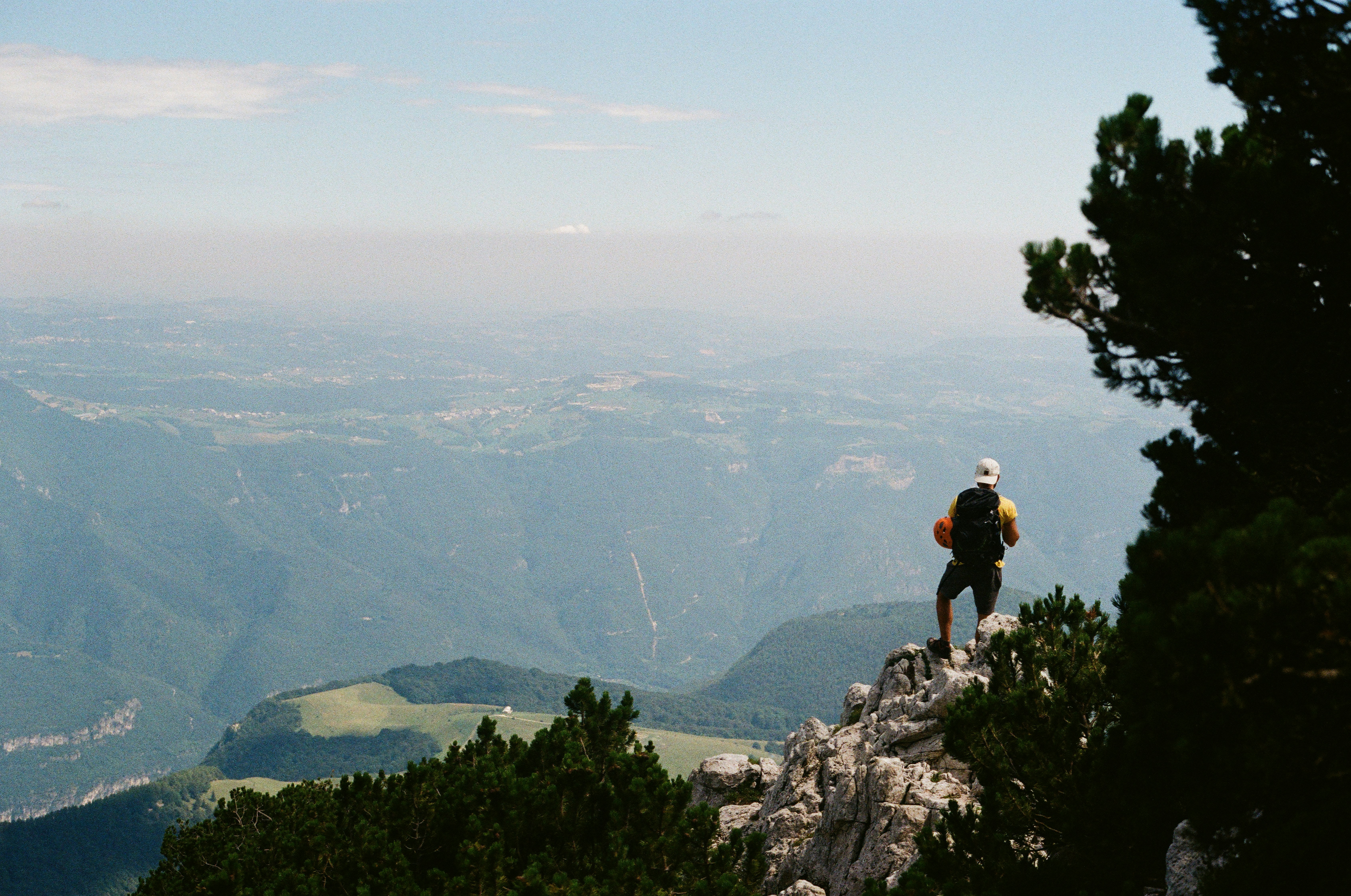 Person in black shirt standing atop a rocky outcrop overlooking a vast landscape during daytime.