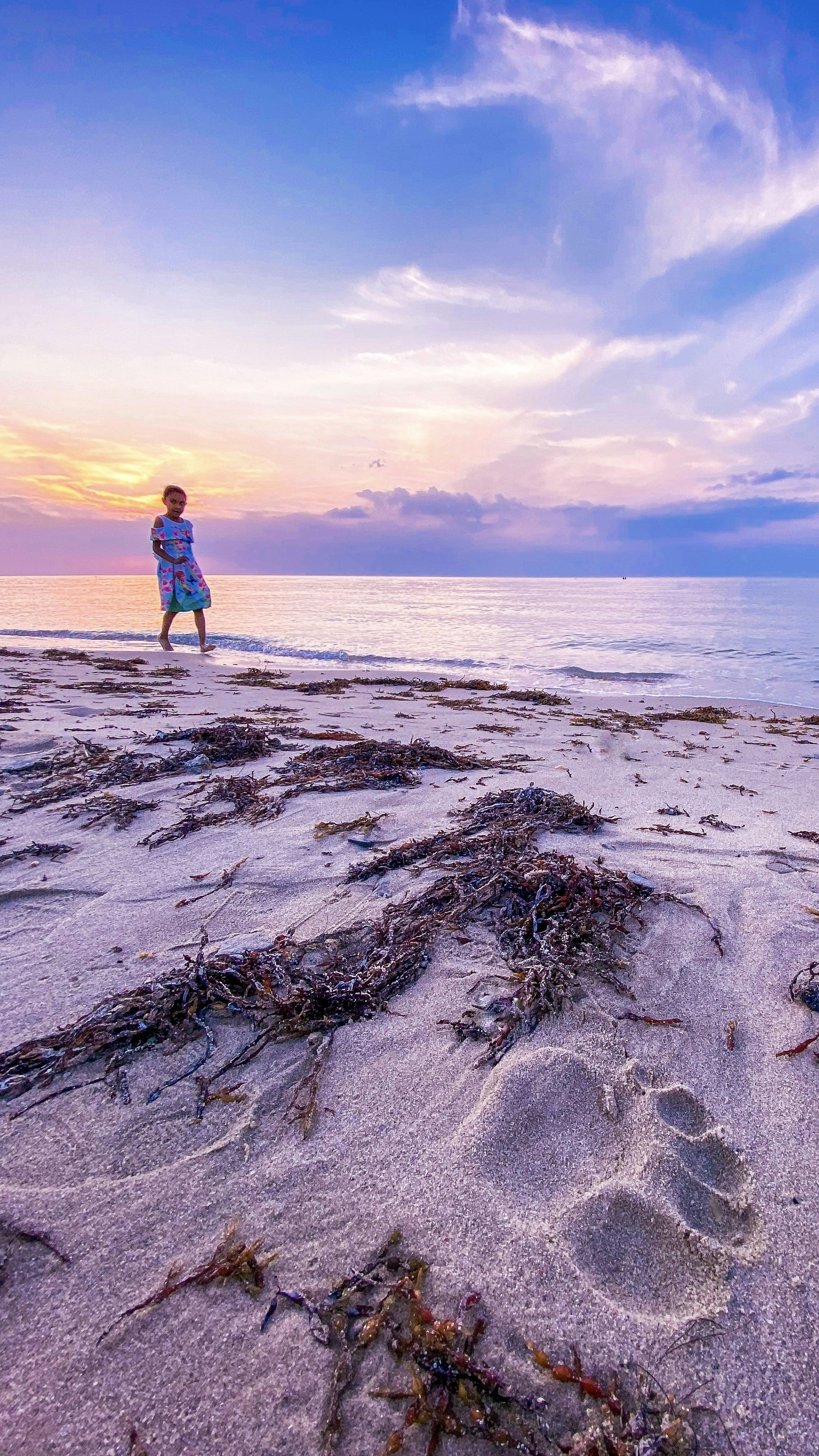 woman in red jacket and blue denim jeans standing on brown sand near body of water
