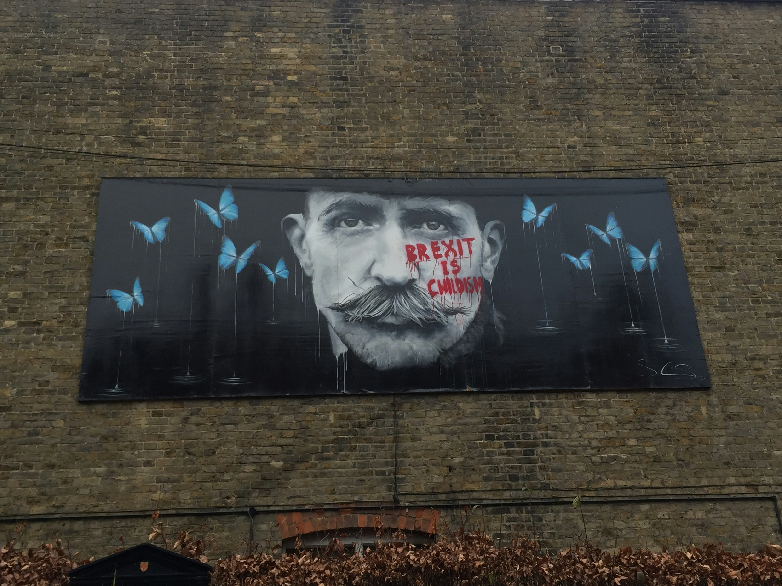 Mural of a man with a mustache surrounded by blue butterflies on a brick wall.
