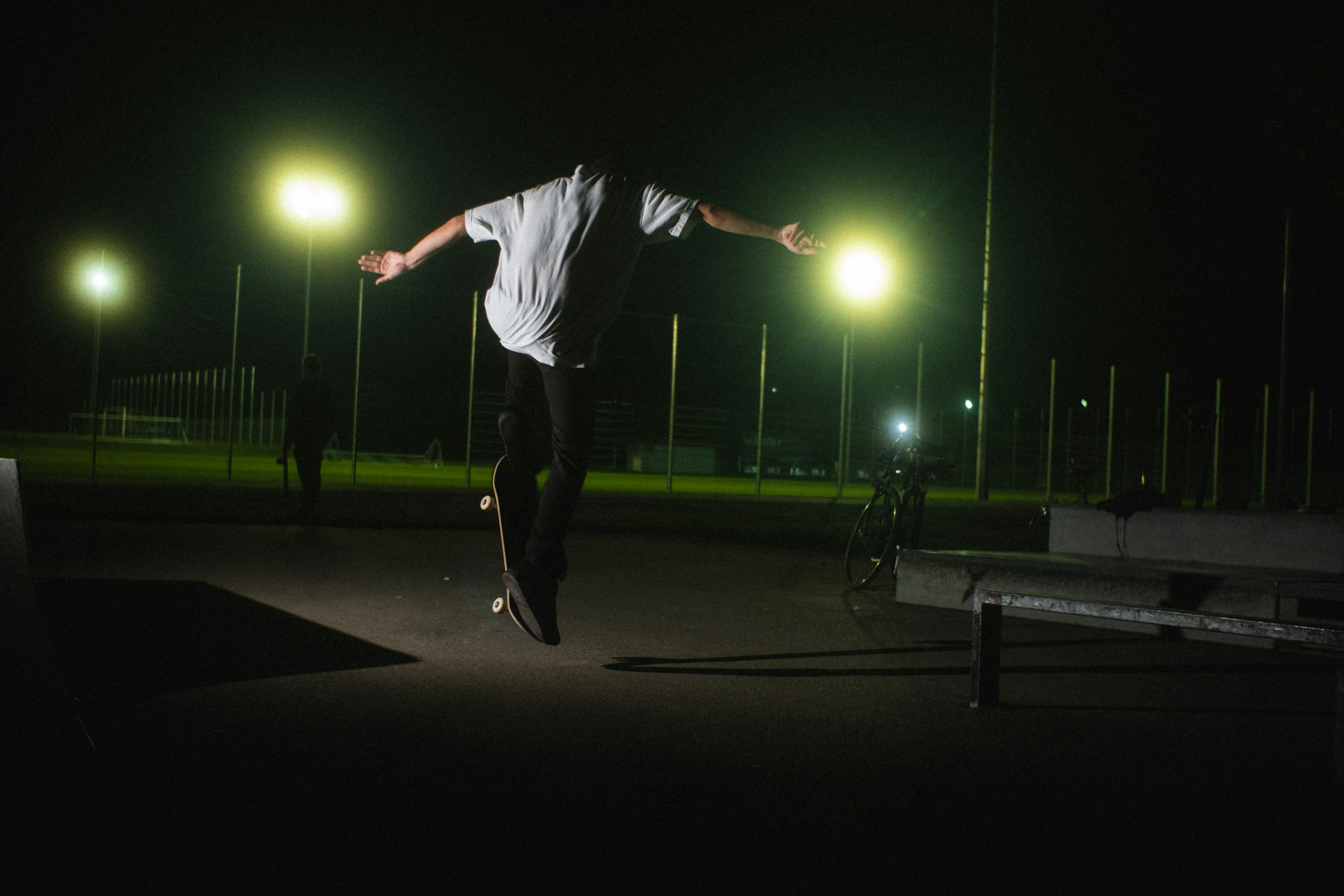 Skateboarder performing a trick under bright floodlights at night, showcasing dynamic motion and energy.