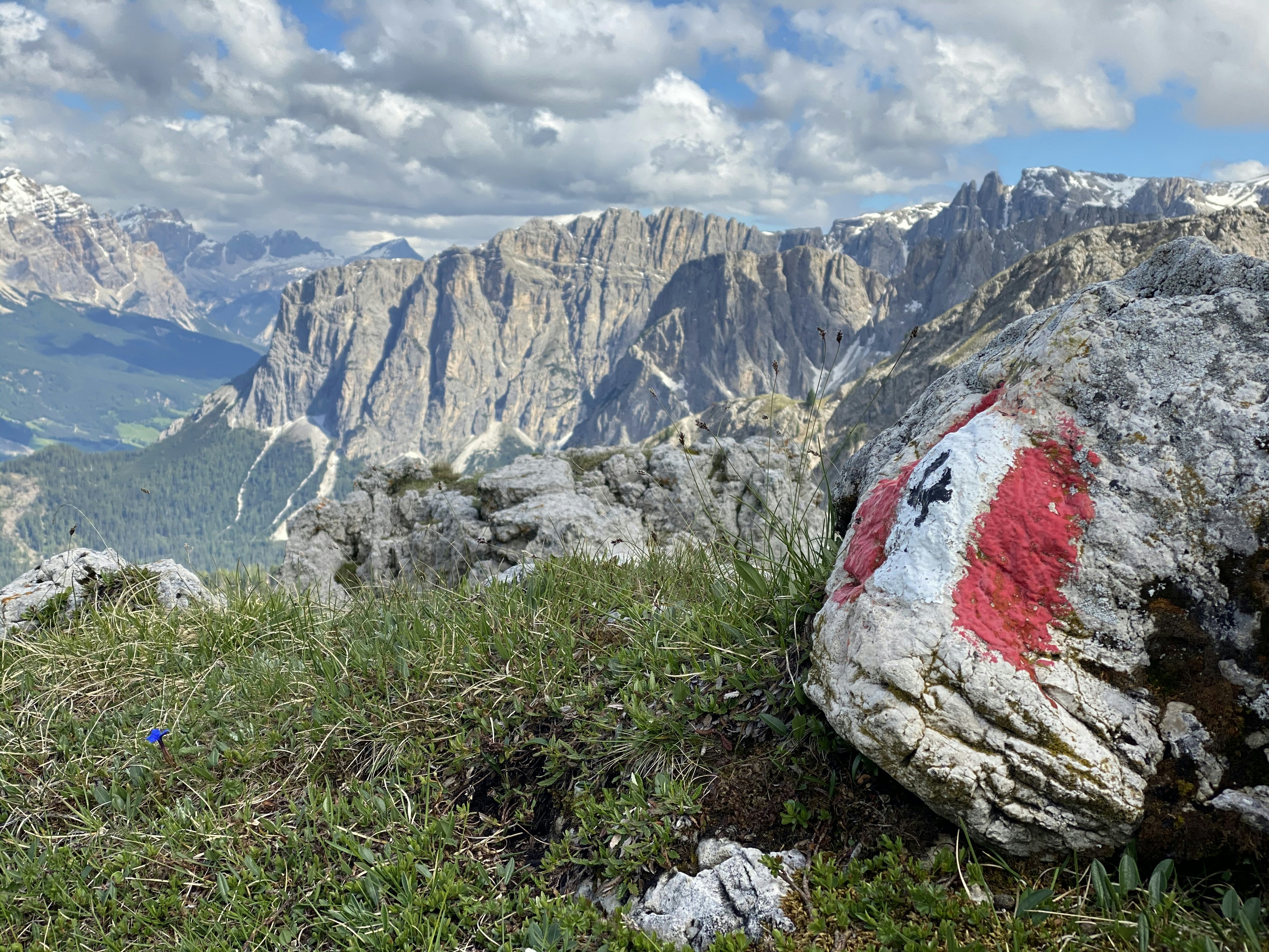 Rock cairn at alpine edge: red-and-white marker gazes toward hanging valleys