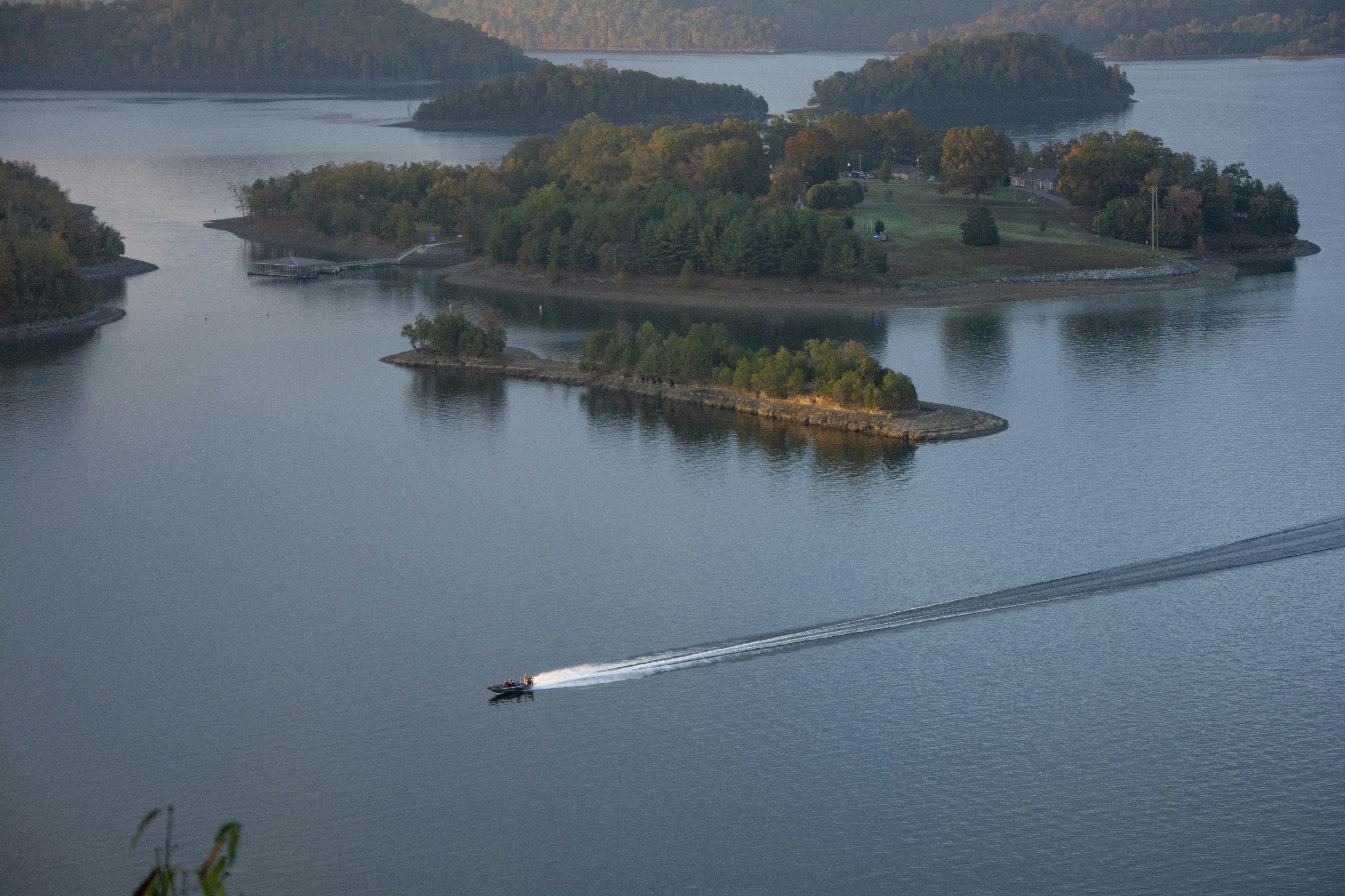Speedboat slicing through calm waters surrounded by autumn-tinted islands under soft evening light.
