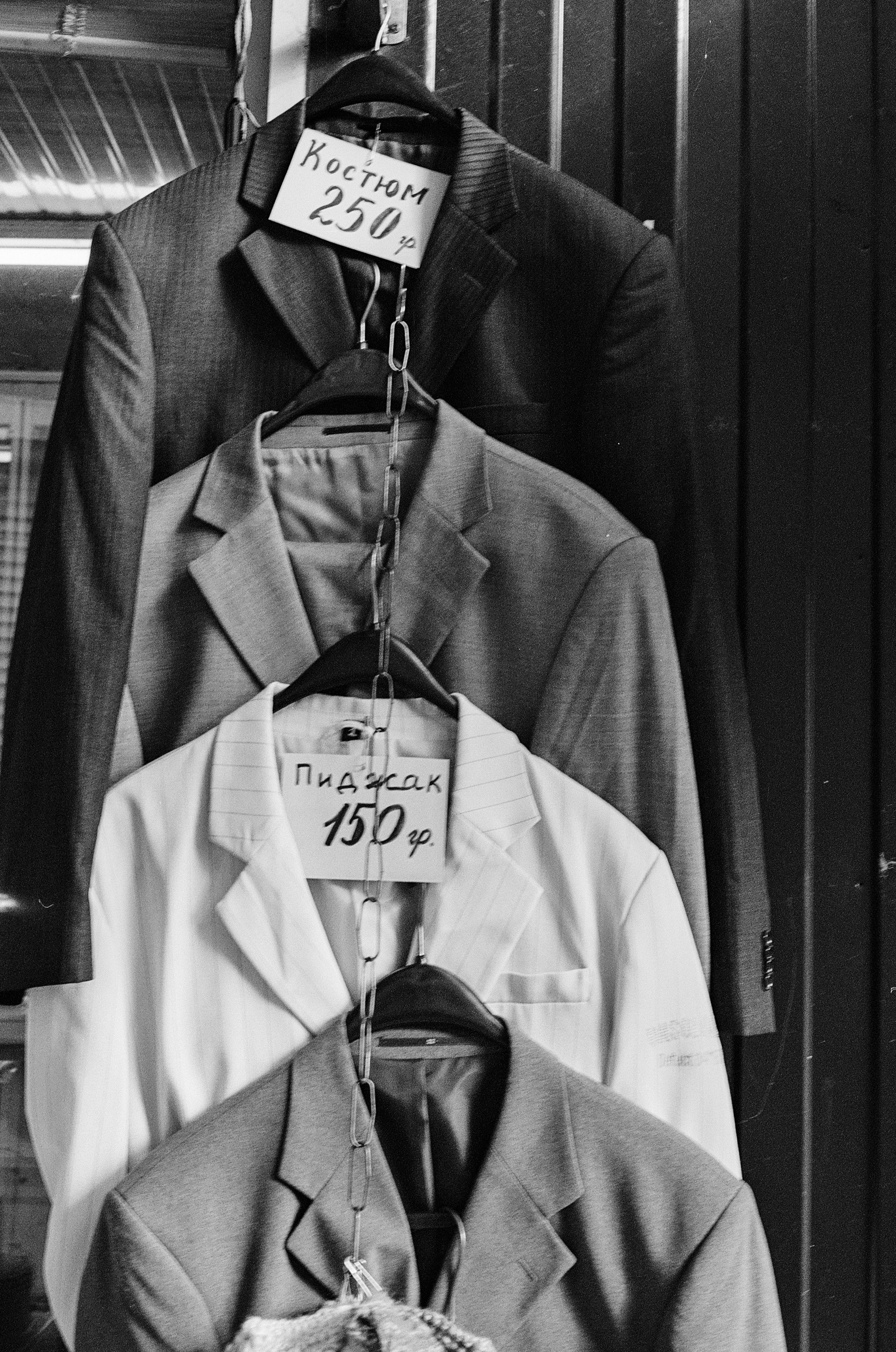 Collection of suits hanging on display, showcasing various styles and prices in a monochrome setting.