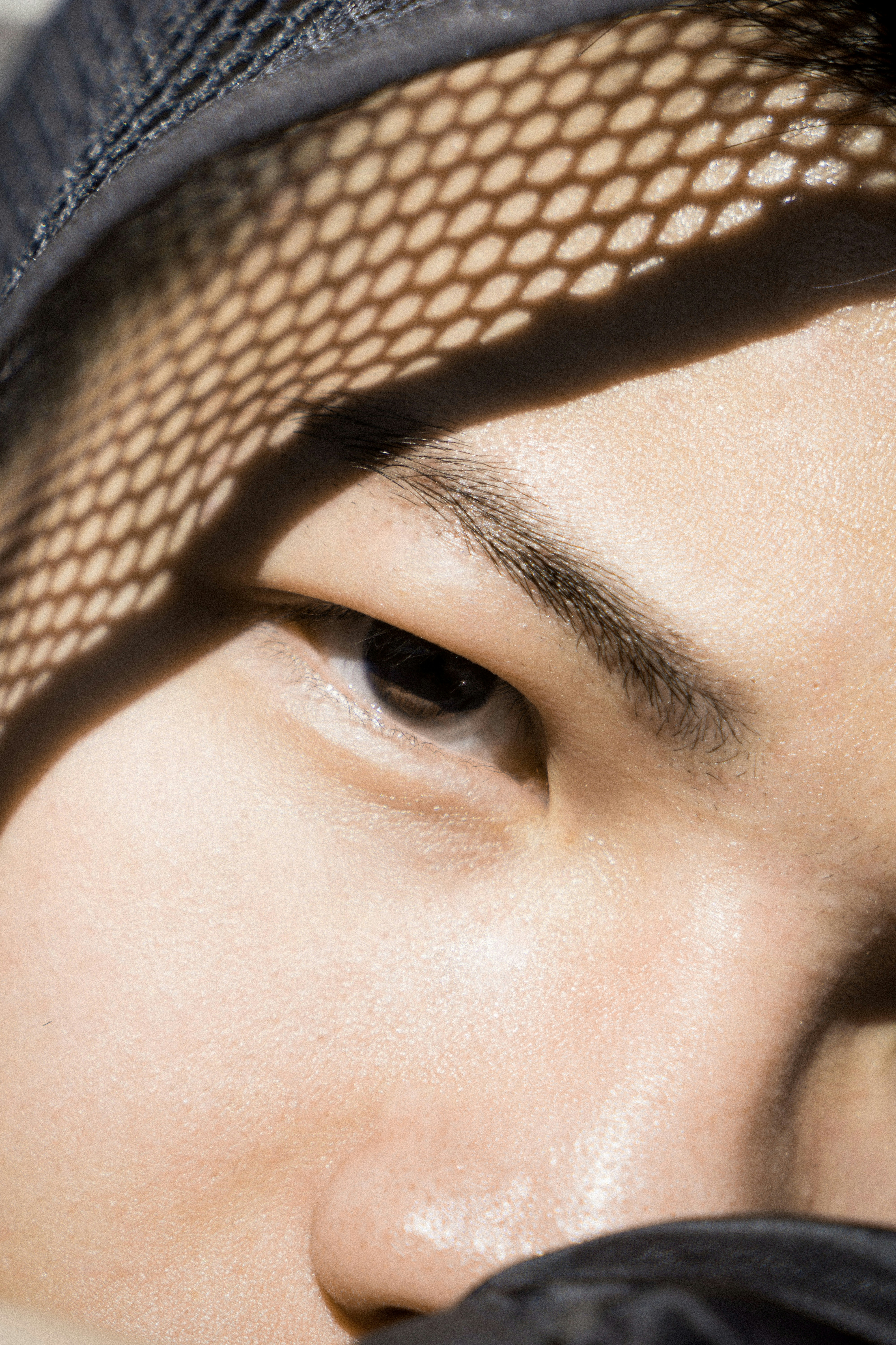 Close-up of a person's eye partially obscured by a mesh fabric, creating intriguing patterns of light and shadow.