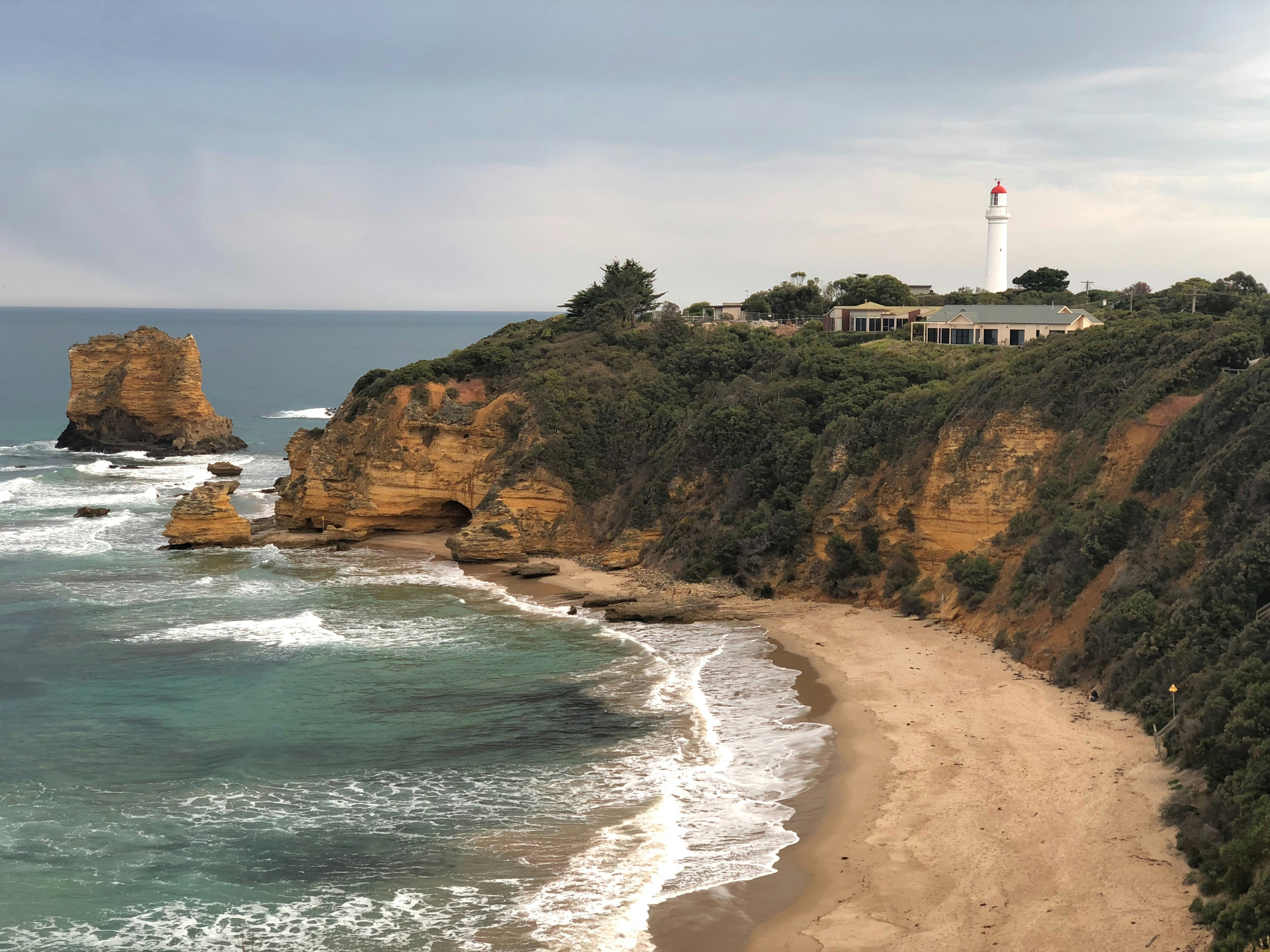 A rugged coastline featuring a lighthouse perched atop a cliff, with waves gently crashing onto a sandy beach below.