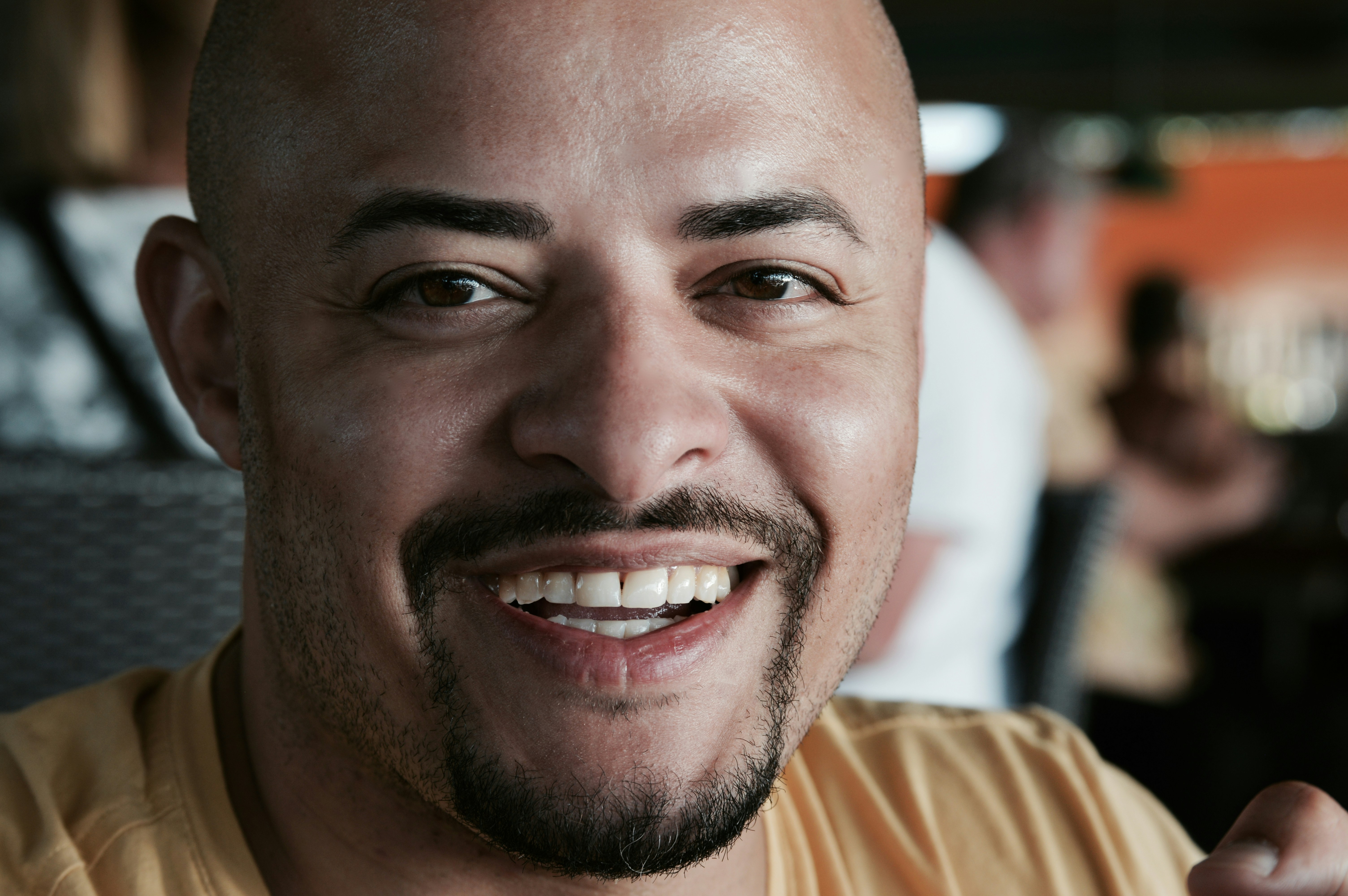 Smiling man with a closely shaved head and a beard, enjoying a moment in a vibrant social environment. His expression conveys warmth and friendliness.