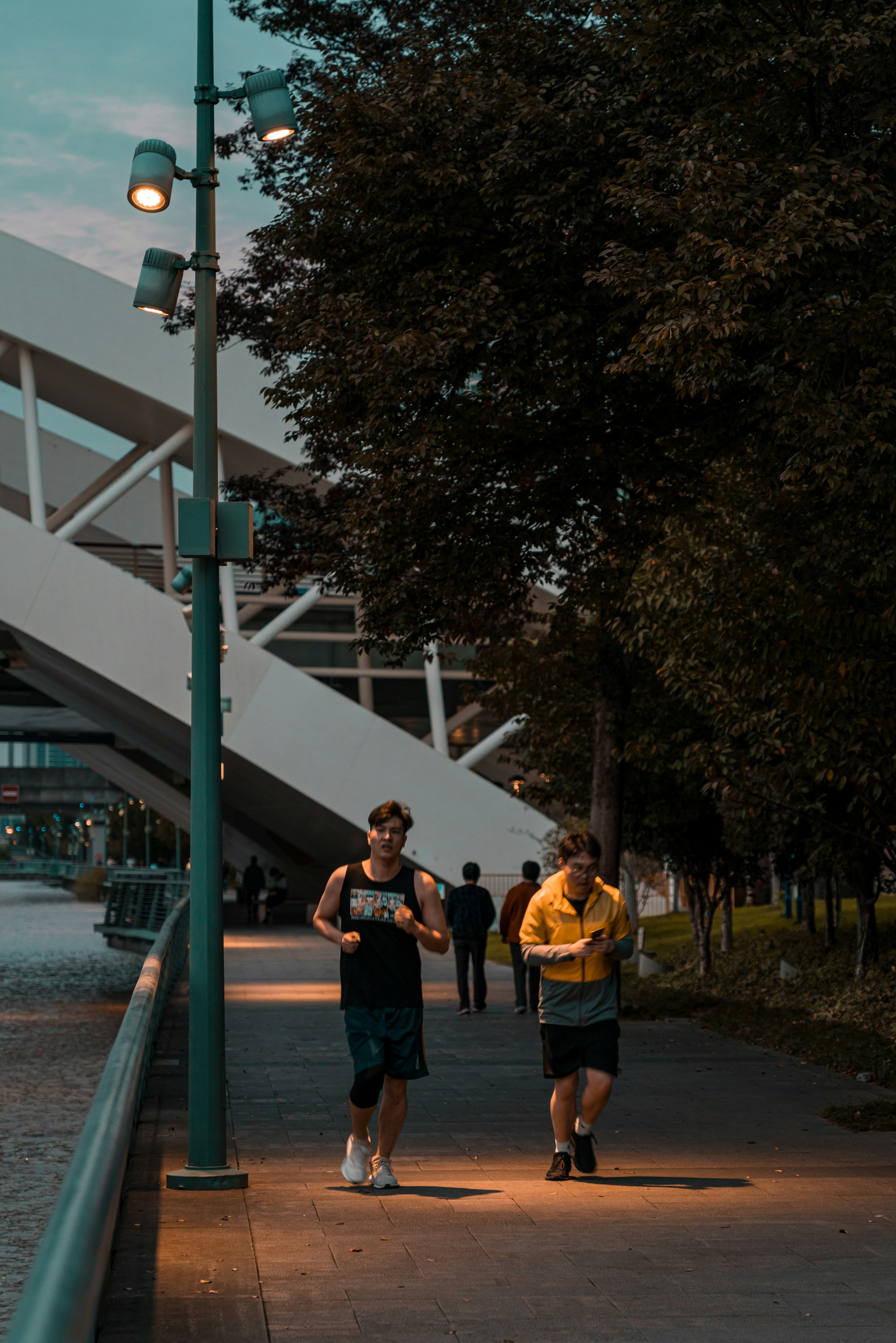 Two runners along a shaded riverwalk at dusk