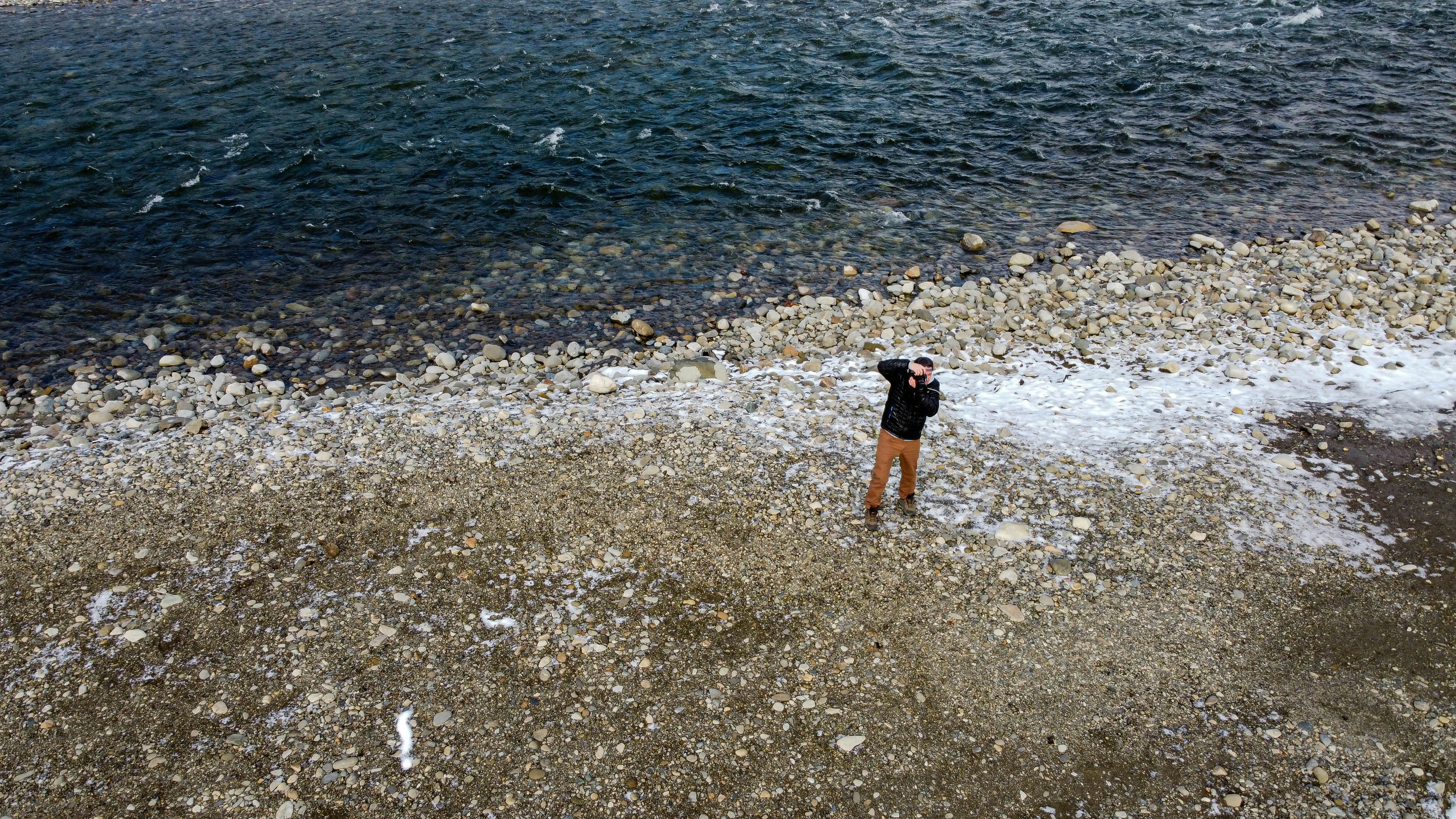 On the Shorebreak: A lone photographer on pebbled coast
