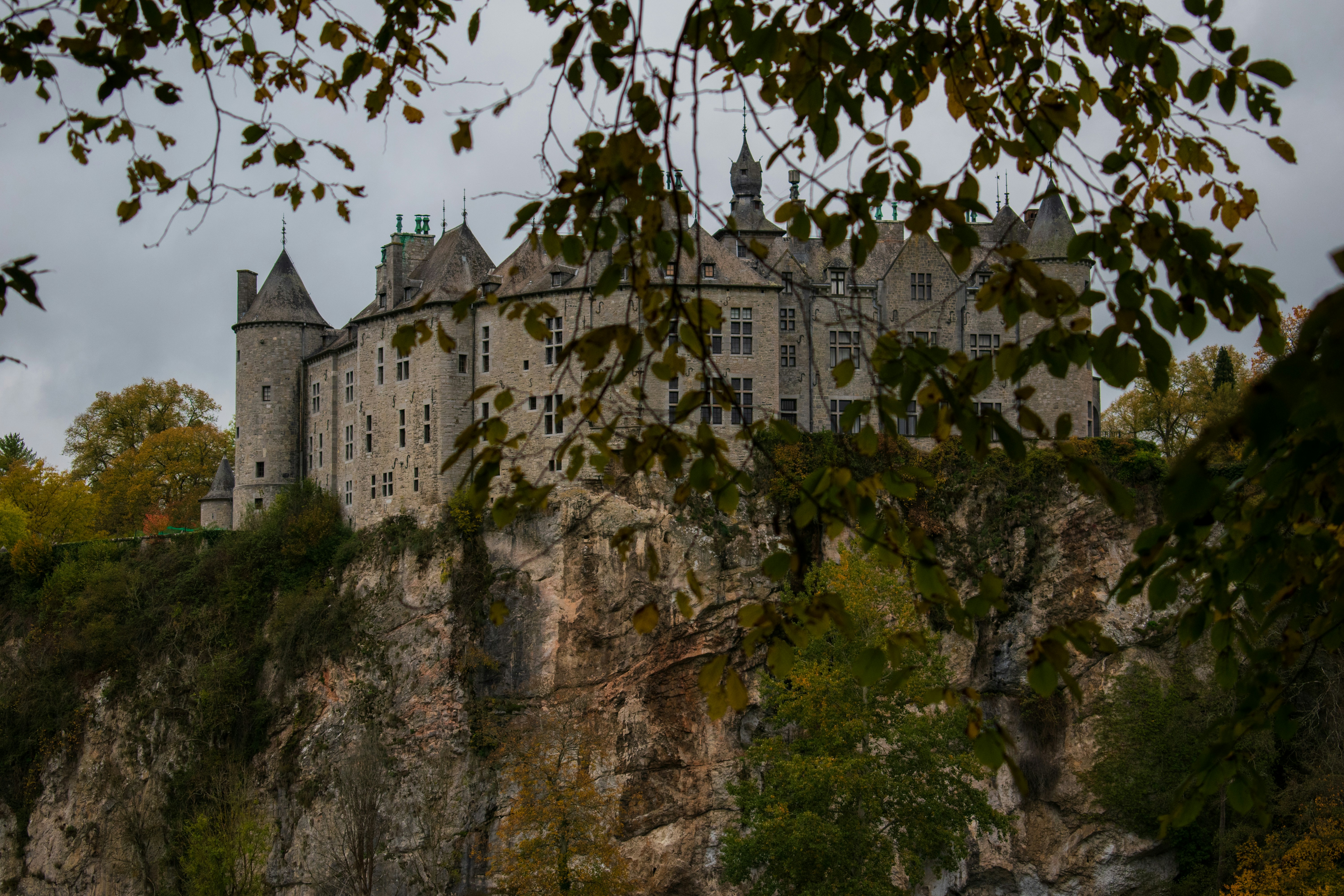 Medieval castle perched atop a rugged cliff, surrounded by autumn foliage and a cloudy sky.