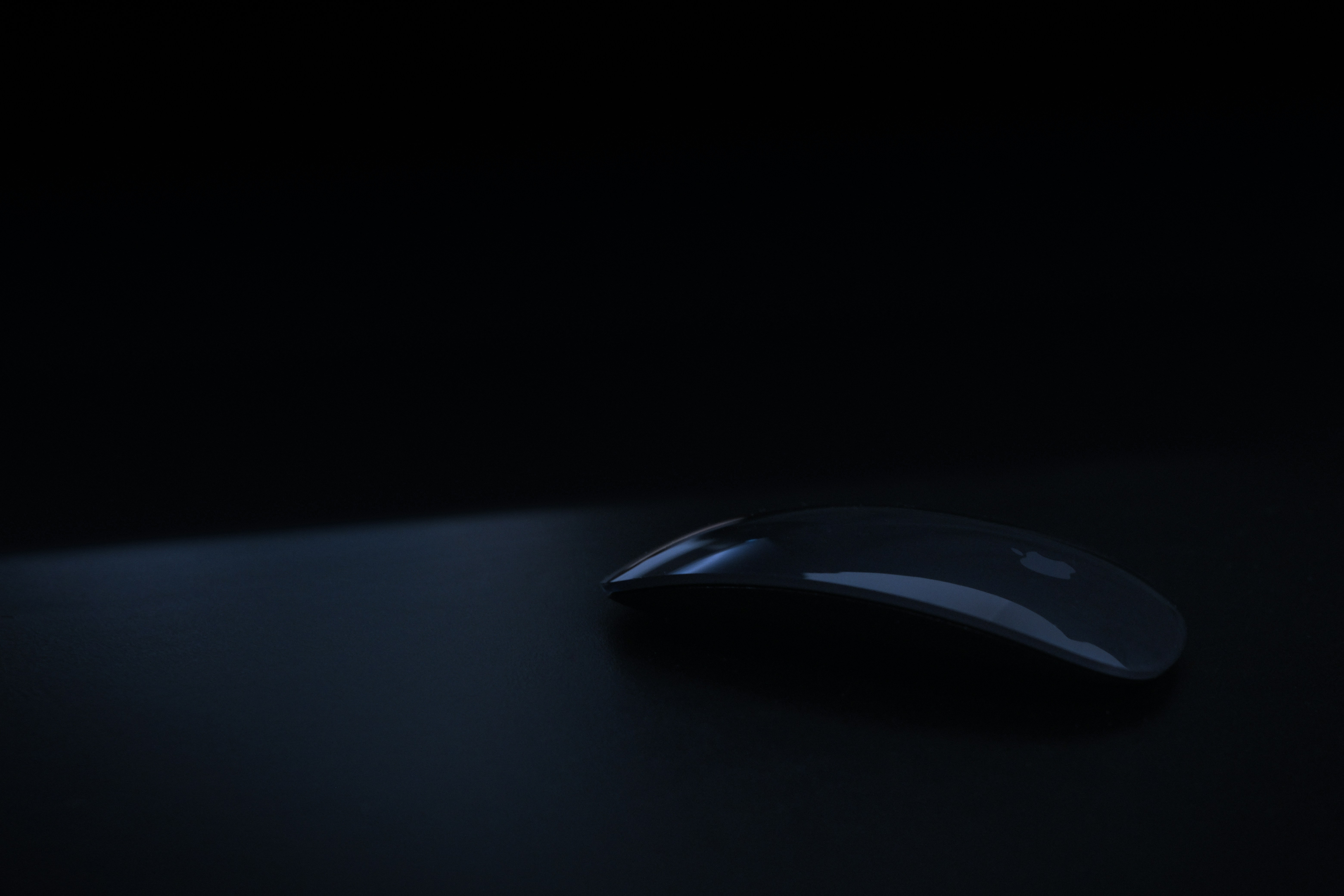 A sleek computer mouse rests on a dark surface, illuminated by a subtle beam of light, emphasizing its smooth curves and minimalist design.