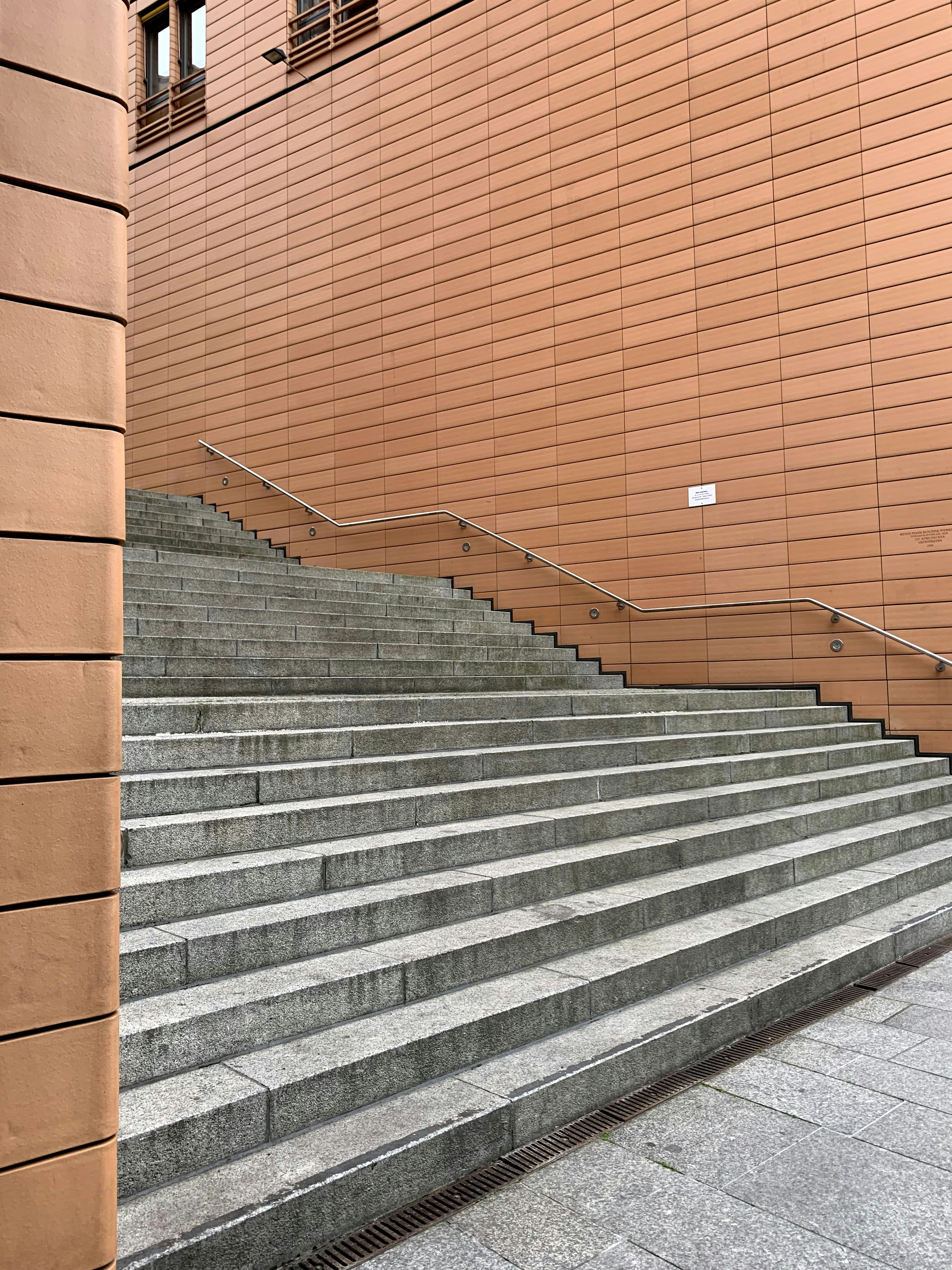 Concrete stairs lead upward against a backdrop of textured orange walls, emphasizing geometric patterns and modern design.