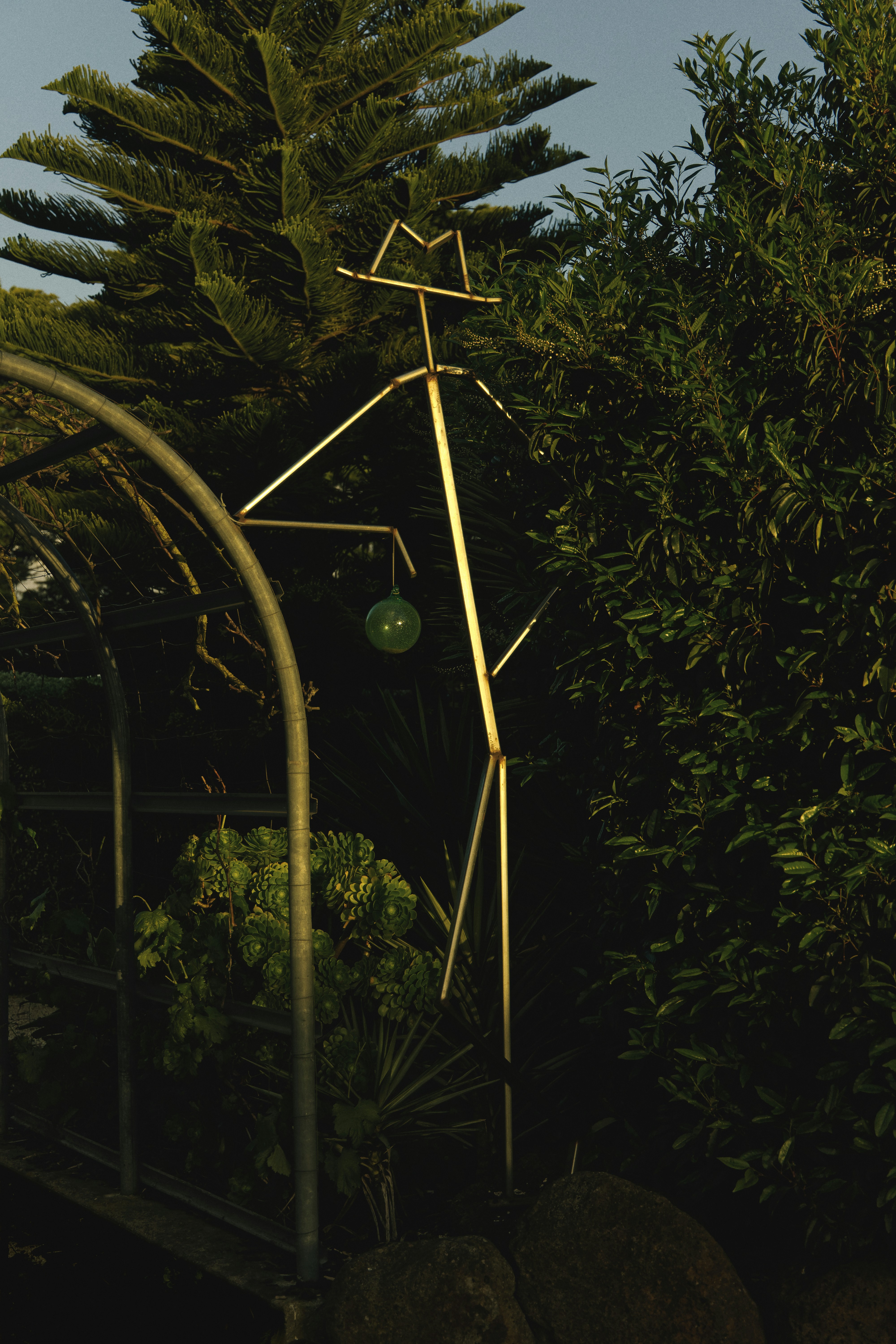 Dusk in the Geometric Garden: A Metal Skeleton Reaching Toward a Green Globe