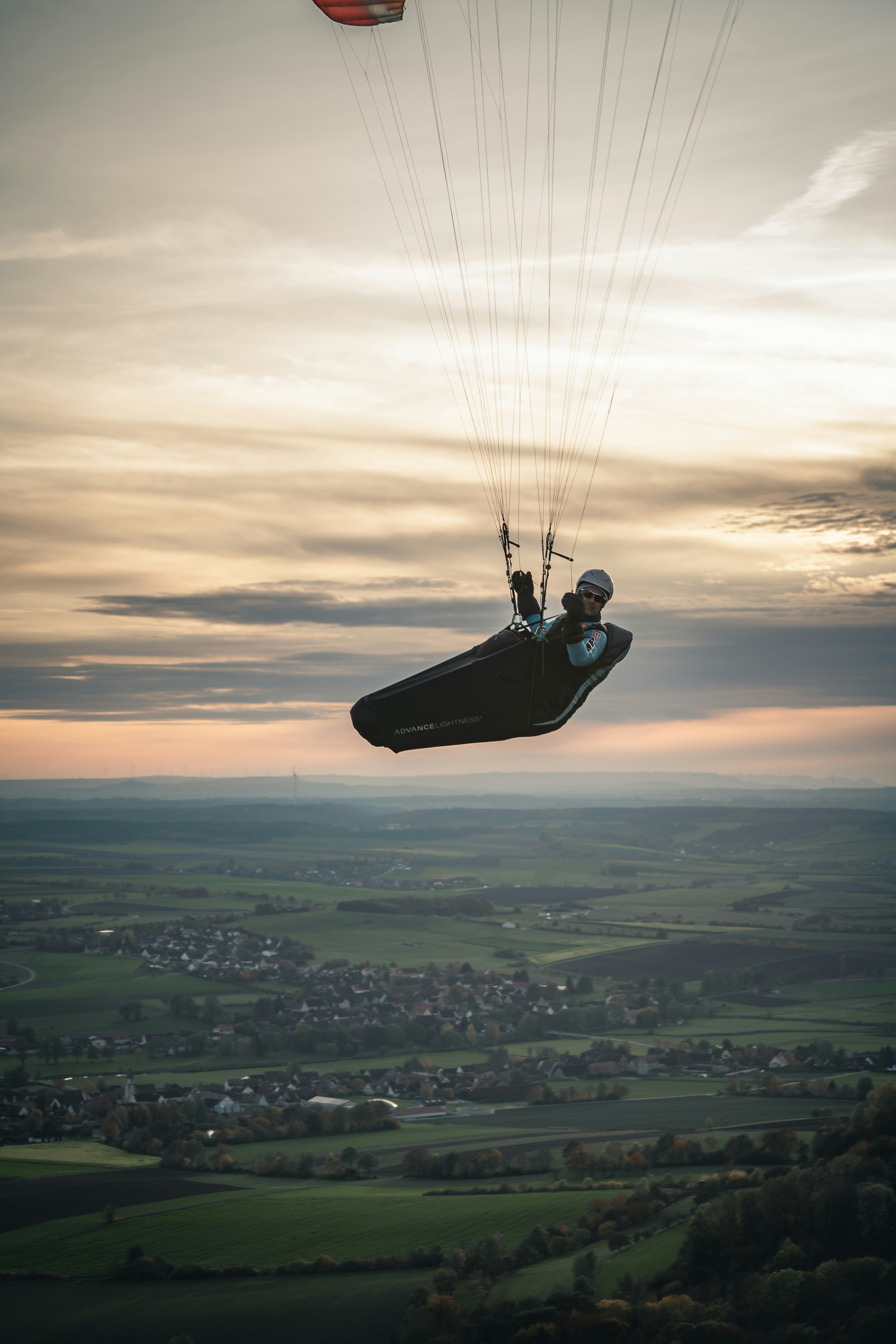 Hovering over patchwork fields: a lone paraglider threading the sunset