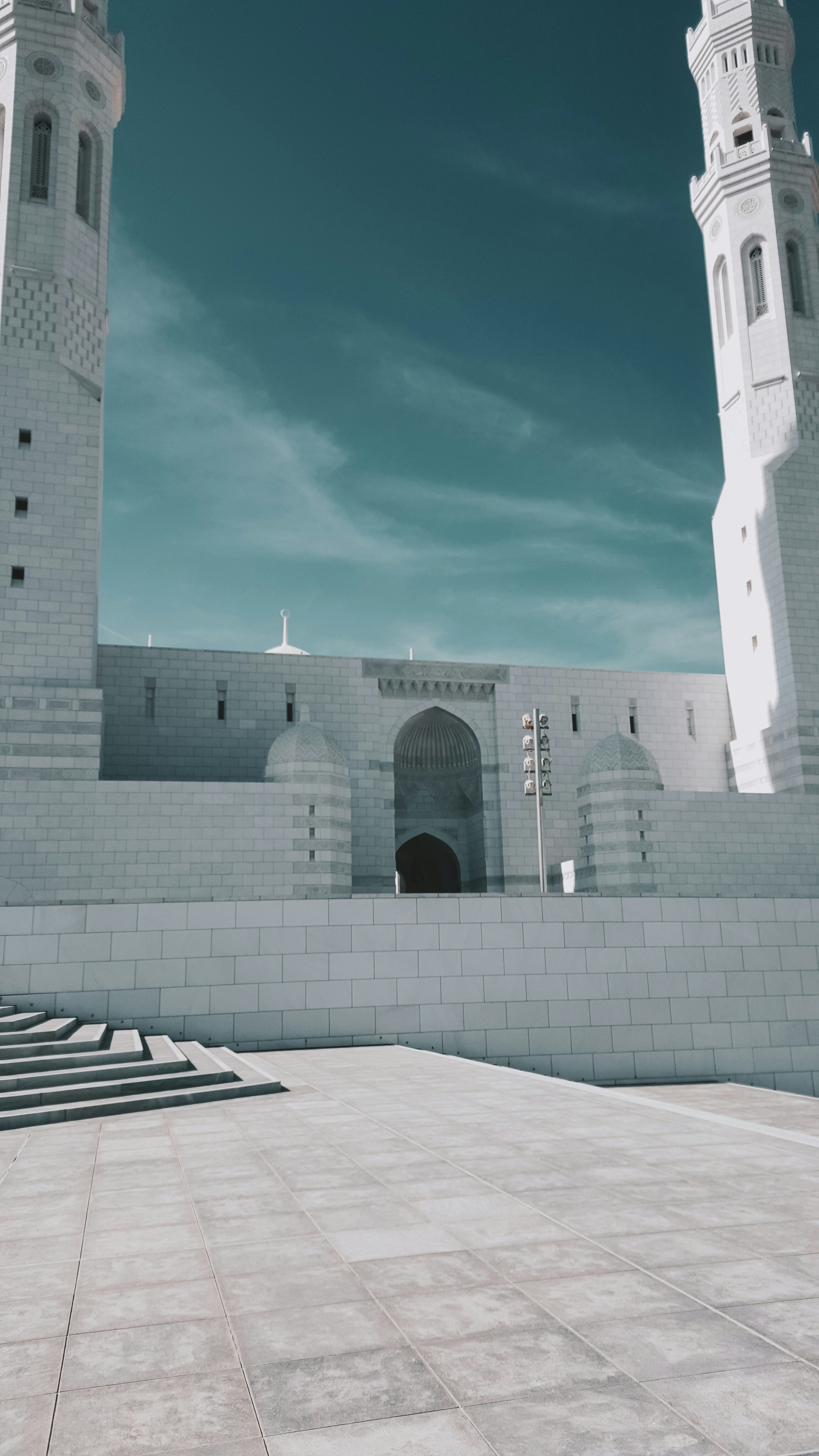 Imposing stone towers flanking a grand entrance, set against a clear blue sky with wispy clouds. The structure showcases intricate architectural details.