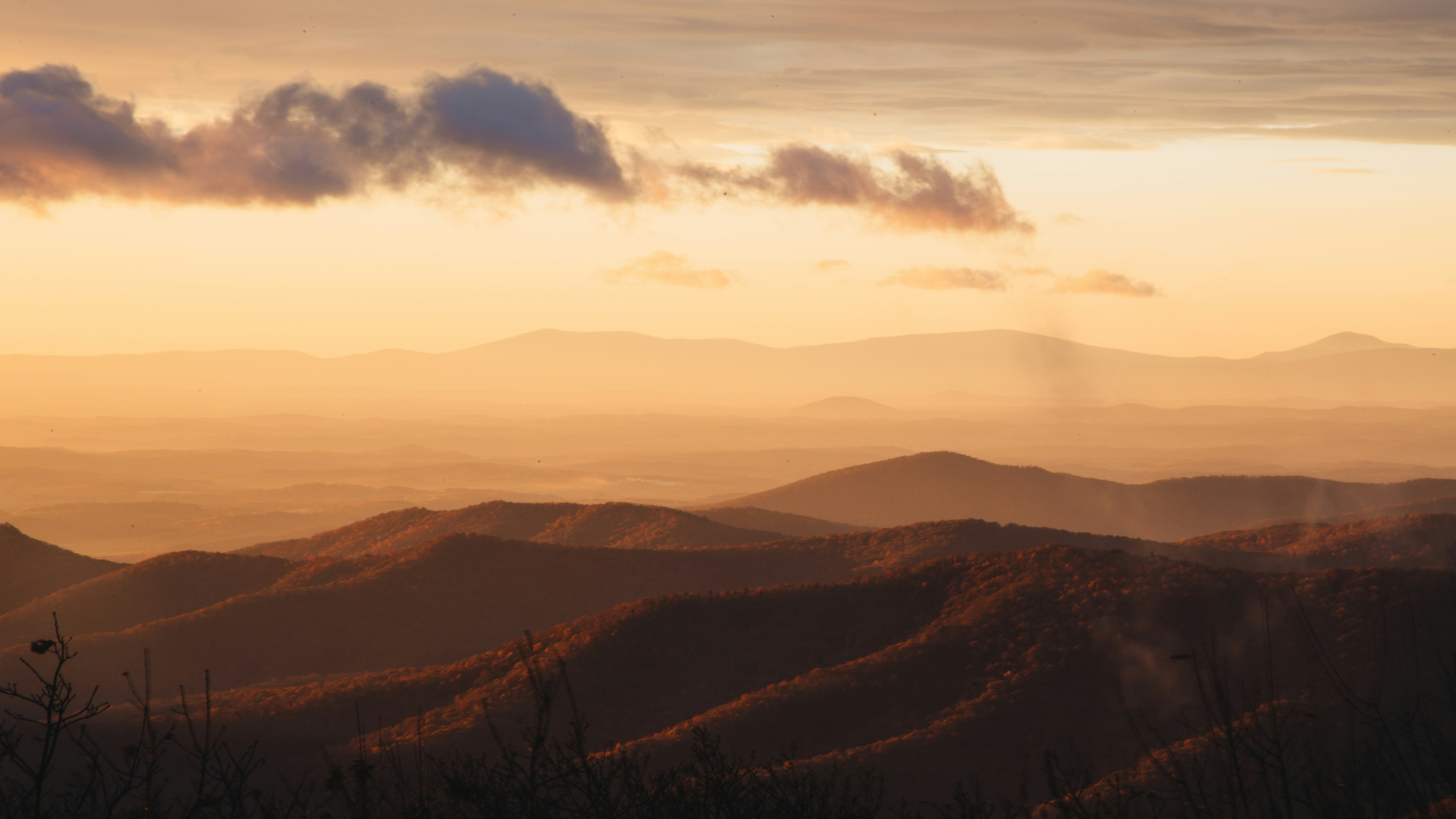Layers of brown mountains under a sky with scattered clouds at sunset.