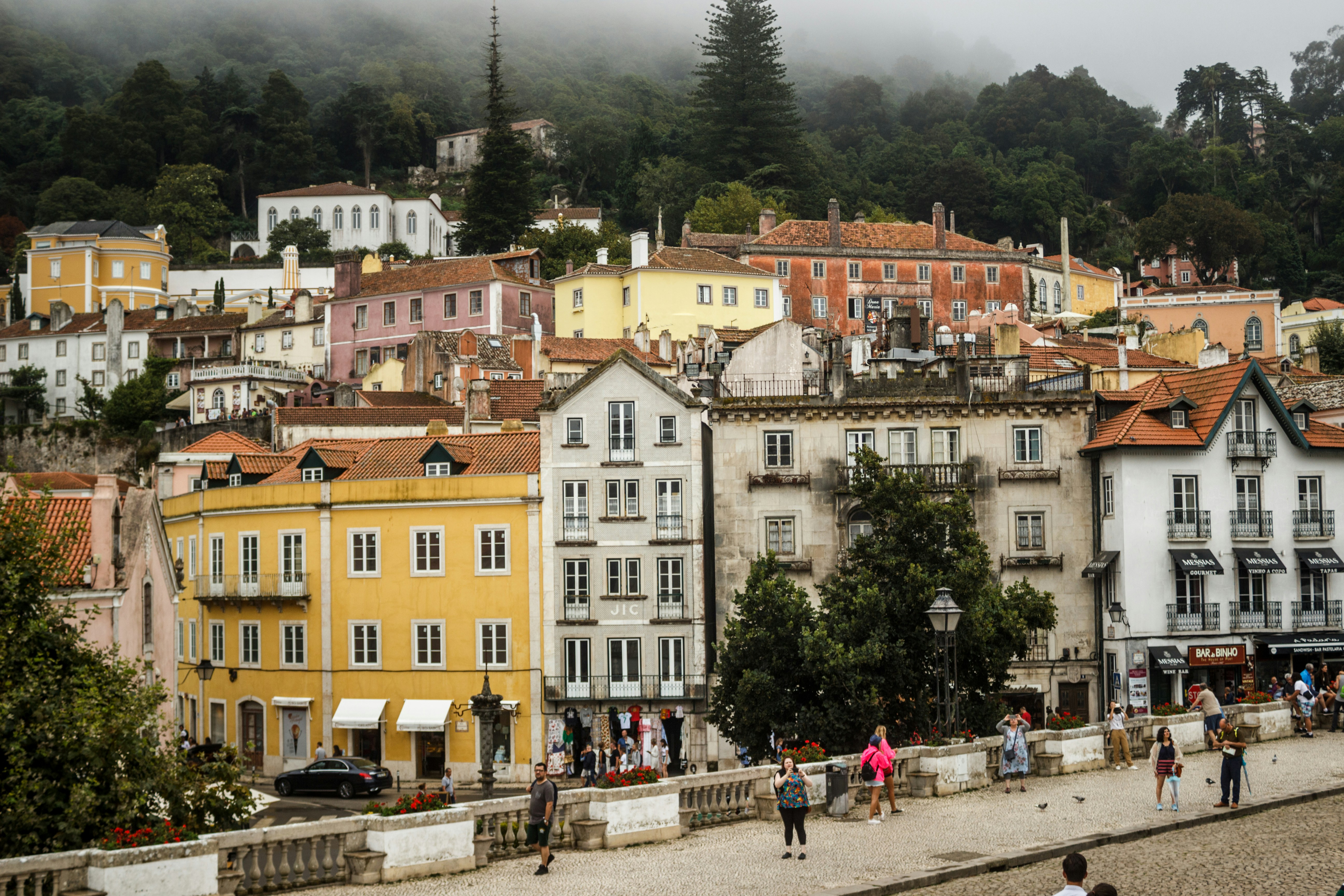 Colorful buildings line the streets of Sintra, showcasing a blend of architectural styles amidst a misty backdrop. The vibrant hues create a lively atmosphere.