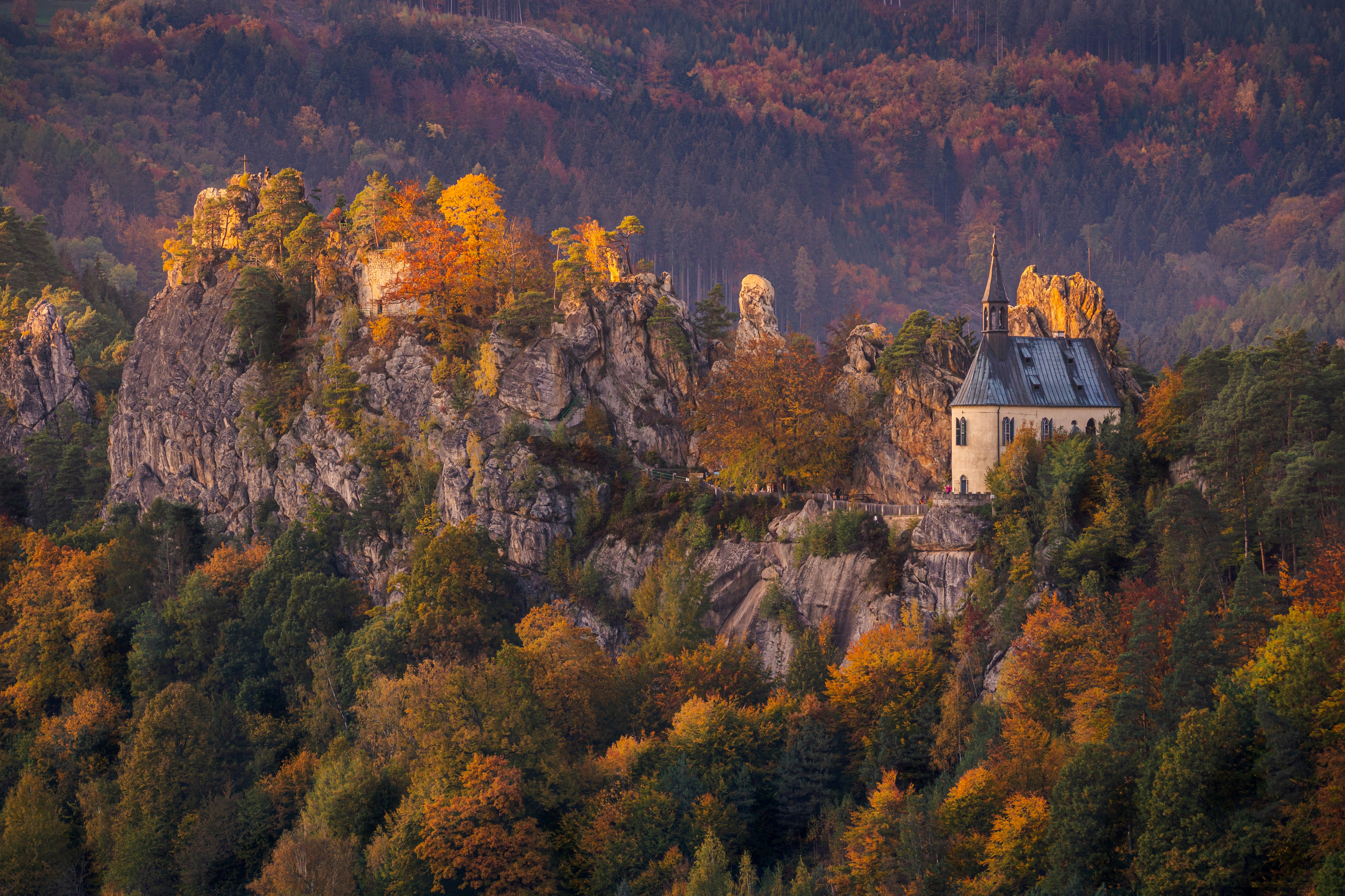 Castle perched on rocky cliffs surrounded by vivid autumn trees.