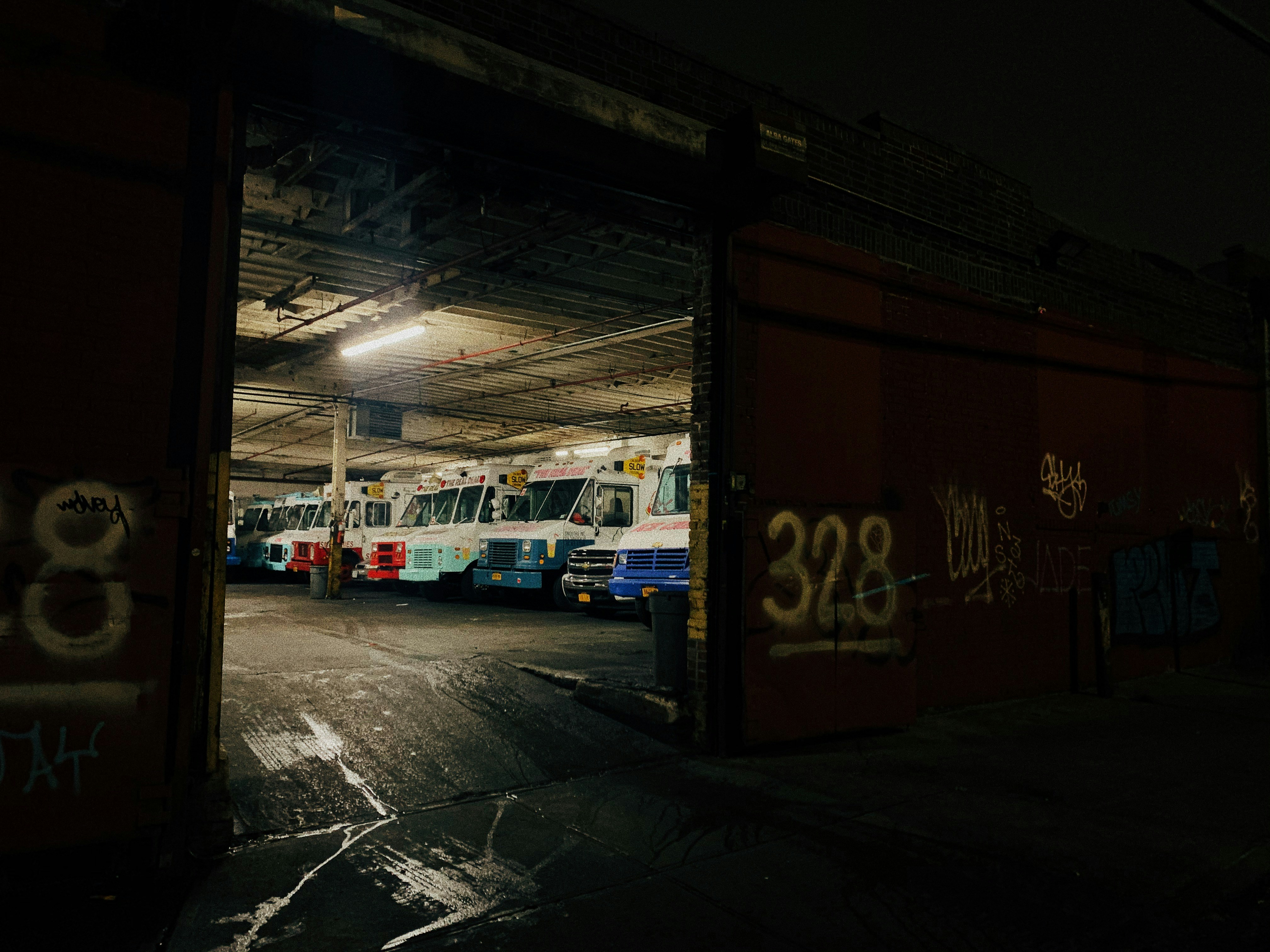 Row of colorful trucks parked inside a dimly lit garage with graffiti-covered walls.