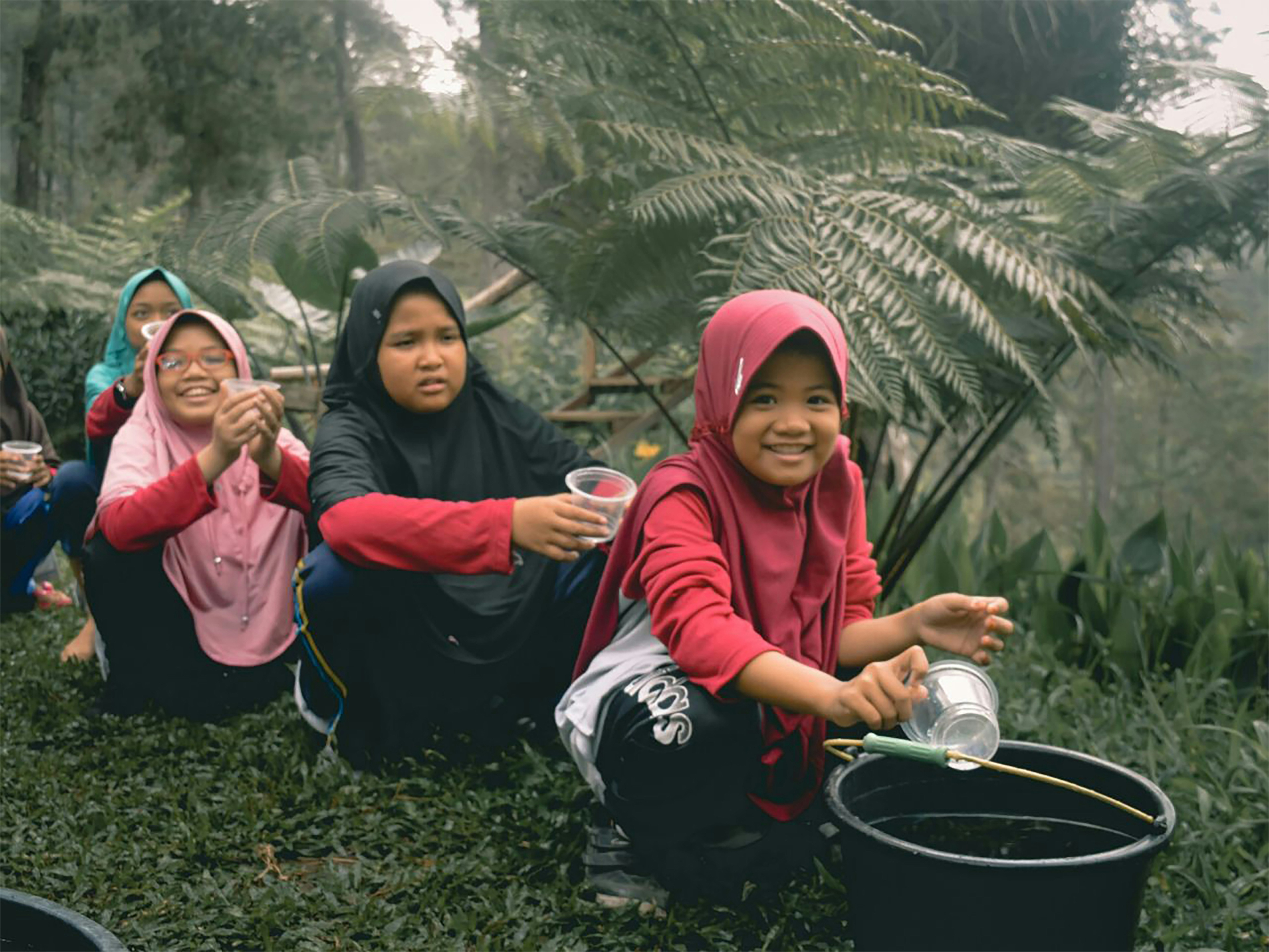 Children in colorful attire engage in outdoor activities surrounded by lush greenery.