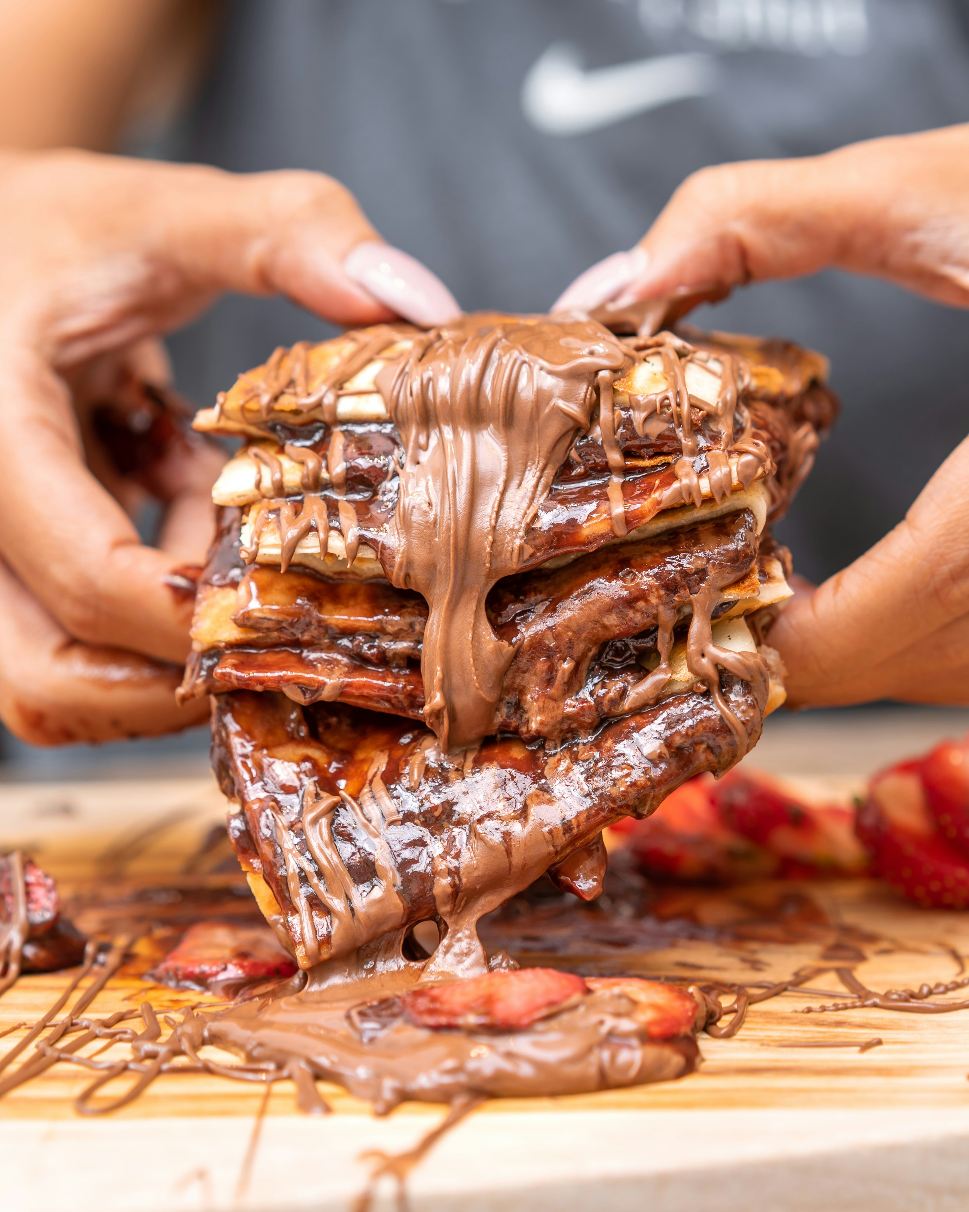 A hands-on approach to a towering dessert, featuring layers of chocolate and strawberries oozing between crispy wafers.