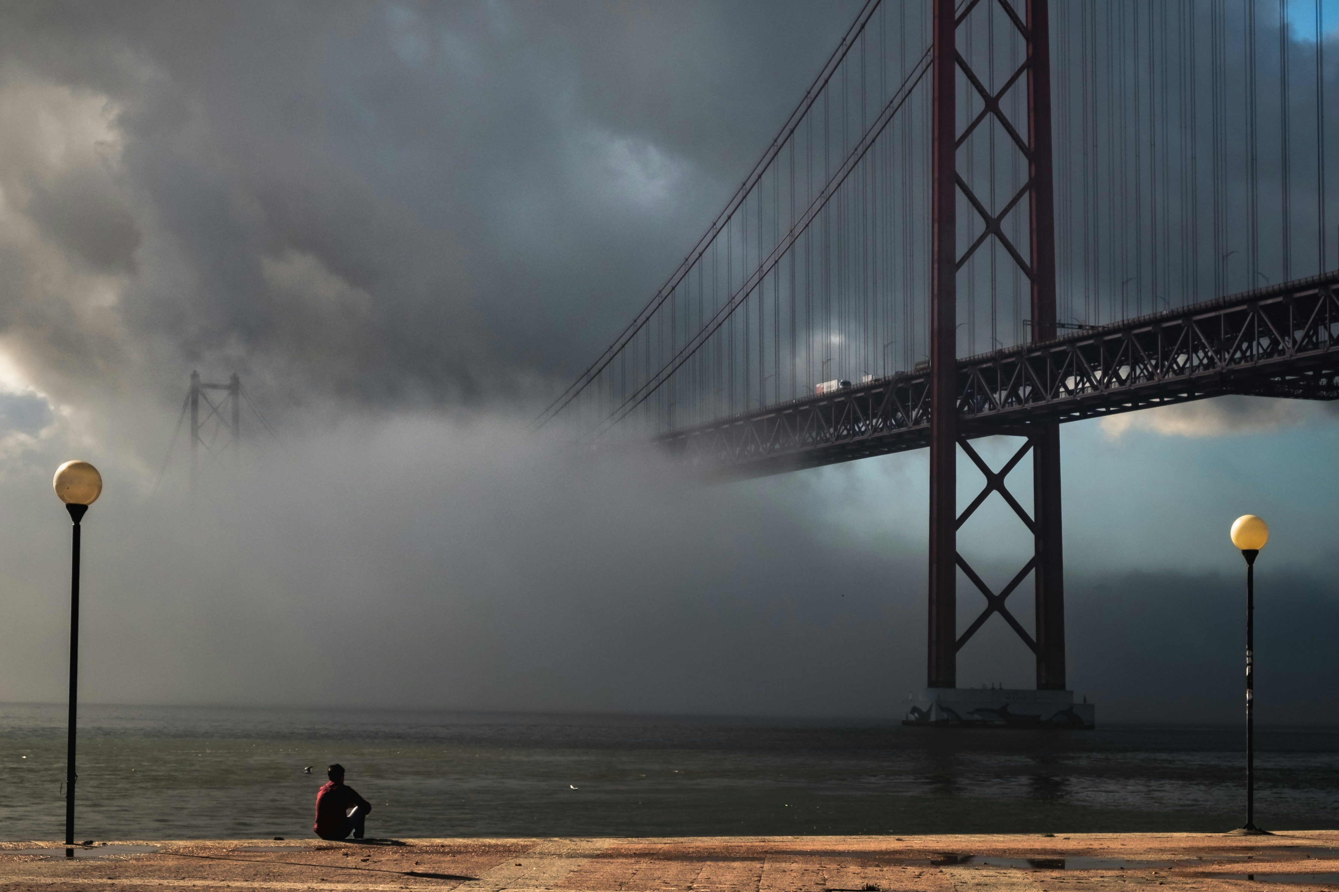 Fog, Bridge, and Solitude: A quiet figure at the quay beneath a massive suspension span