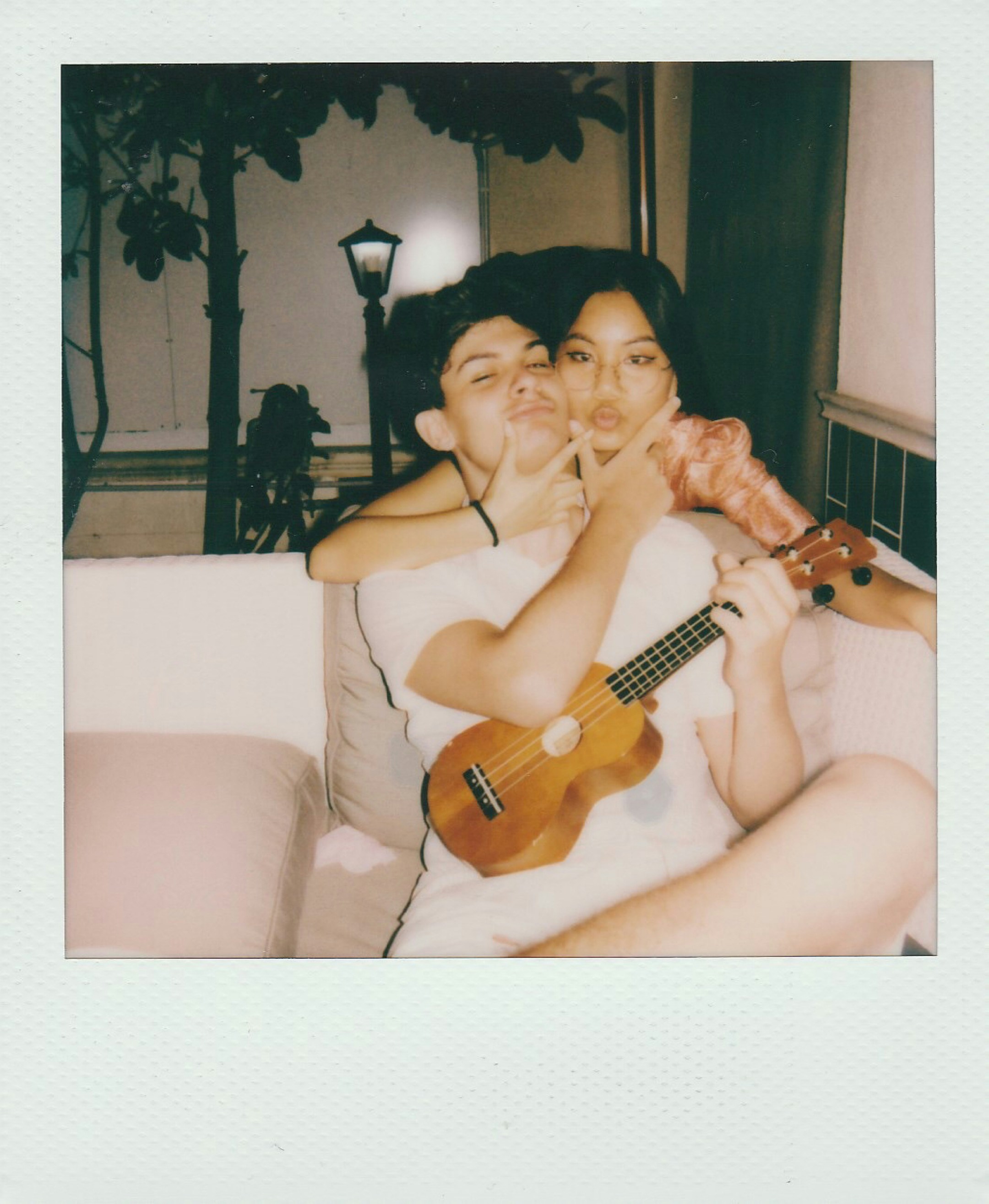 Two friends playfully posing with a ukulele, showcasing a lighthearted moment in a cozy setting.