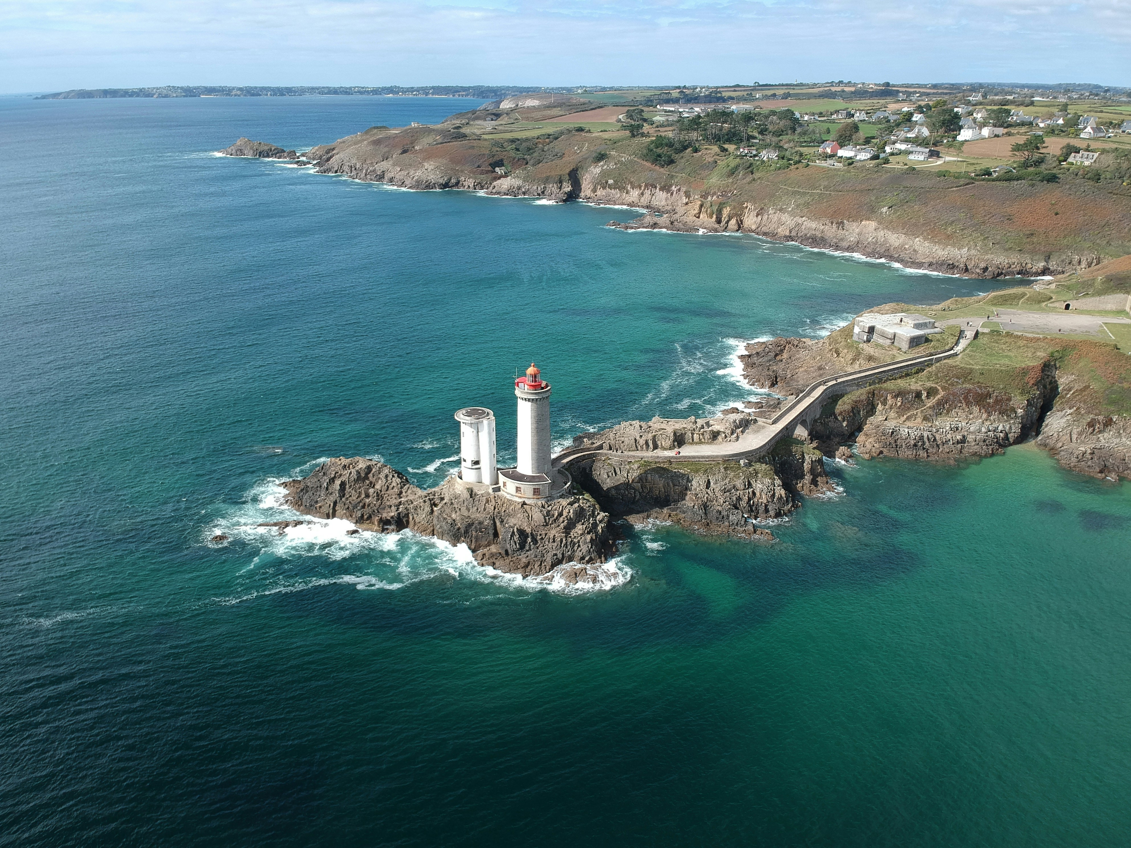Lighthouse perched on a rocky promontory surrounded by turquoise sea and rugged cliffs.