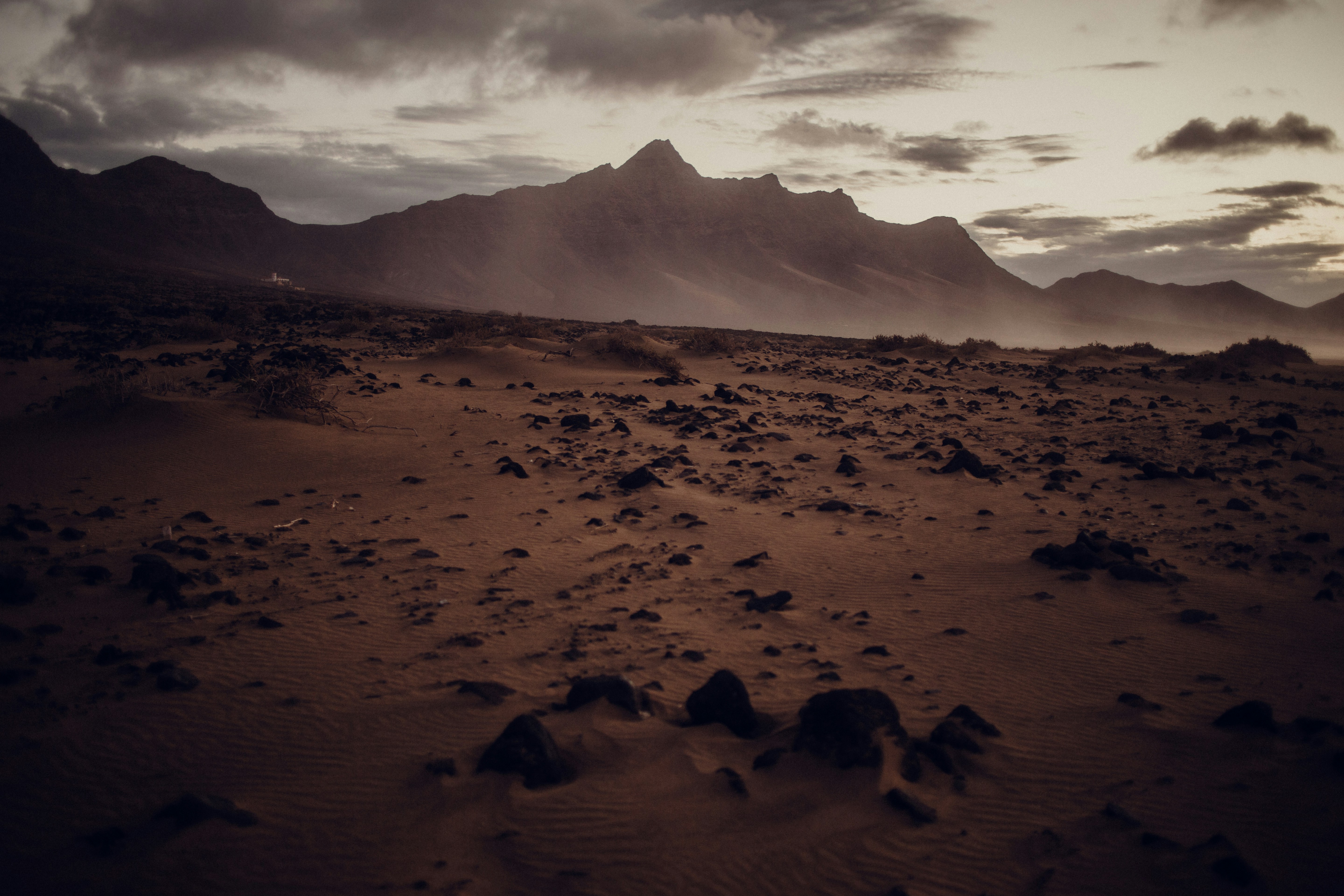 Windswept desert landscape with rugged mountains under a moody sky.
