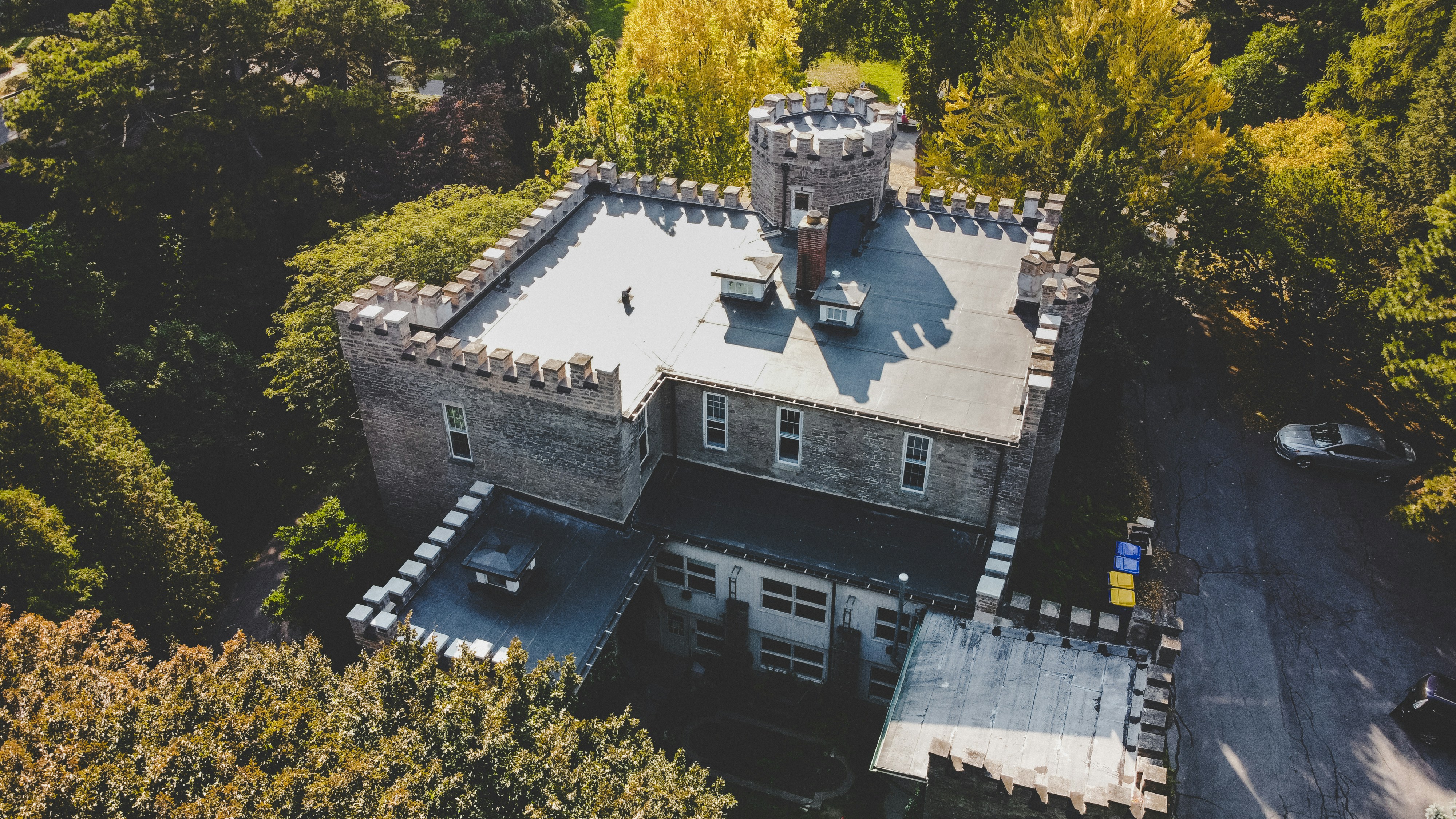 Historic stone castle nestled among vibrant trees, showcasing a unique architectural design with a turret. A glimpse into a serene outdoor setting.