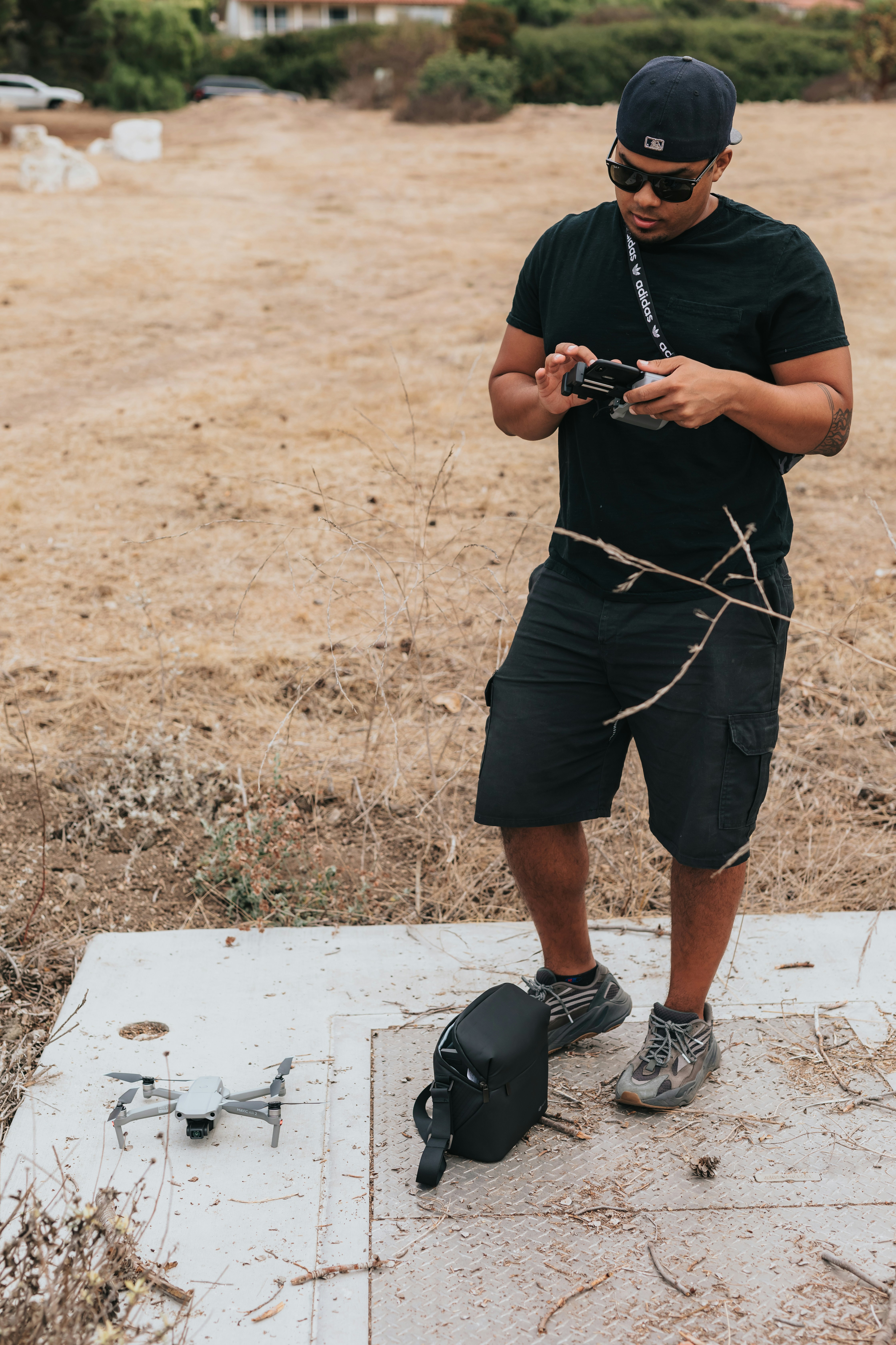 Operator in the Field: A Drone Controller Stands Ready beside a Drone on a Trash-blanket Concrete Pad
