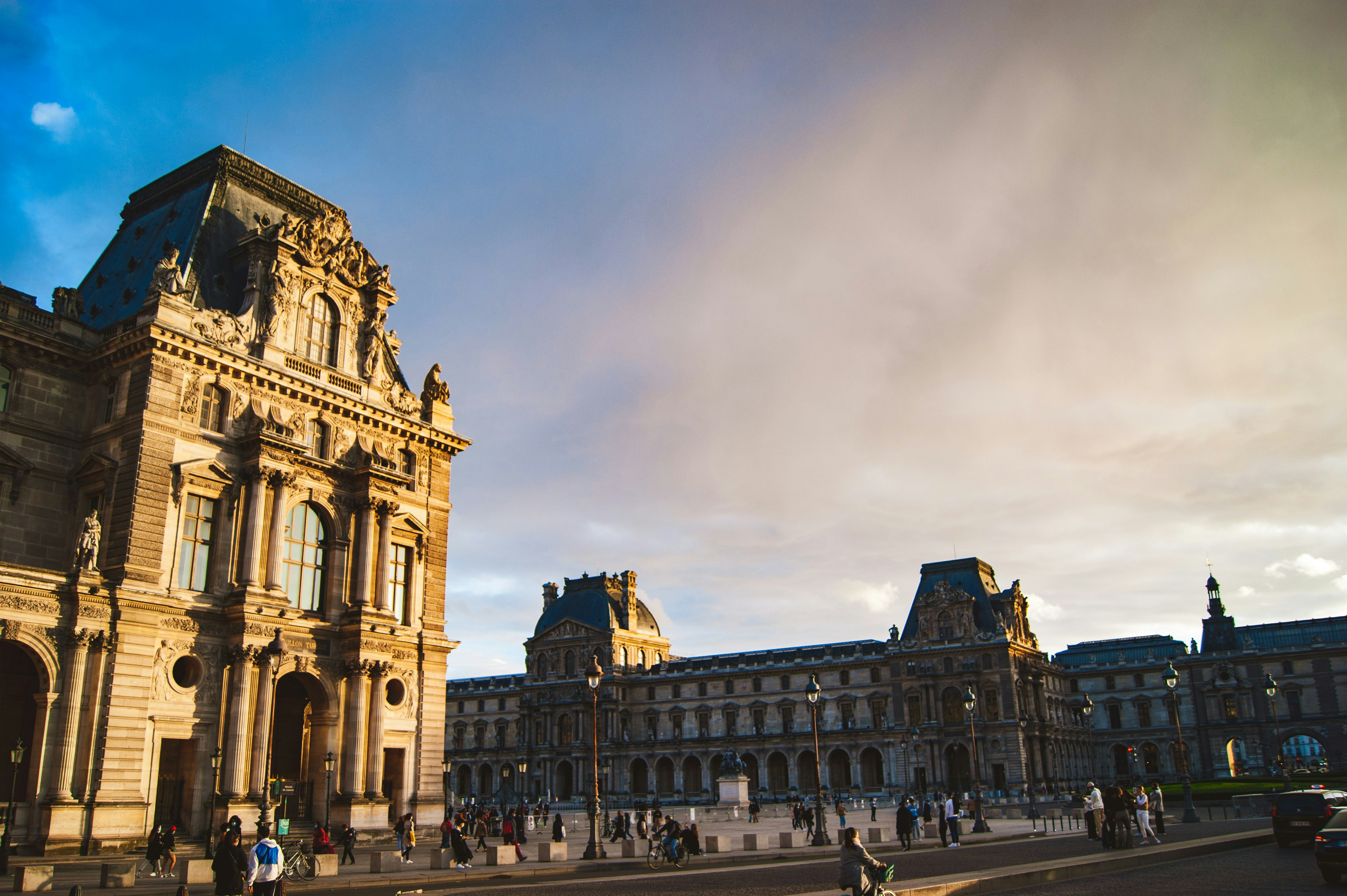 Grand architectural details of the Louvre Museum bathed in warm light, with visitors exploring the iconic site.