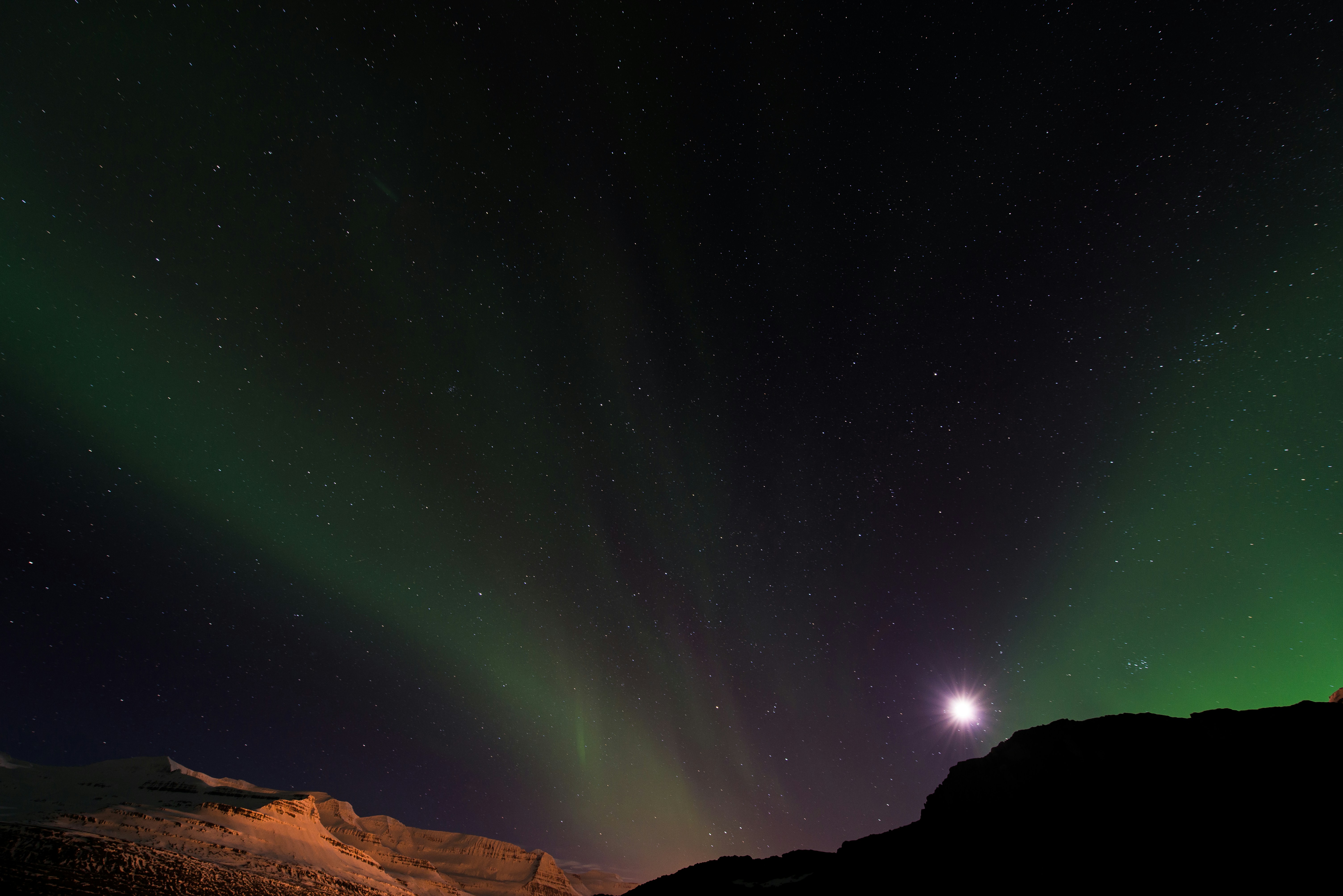 Aurora Drapes the Night Over a Snow-Capped Ridge Beneath a Star-Pocked Sky