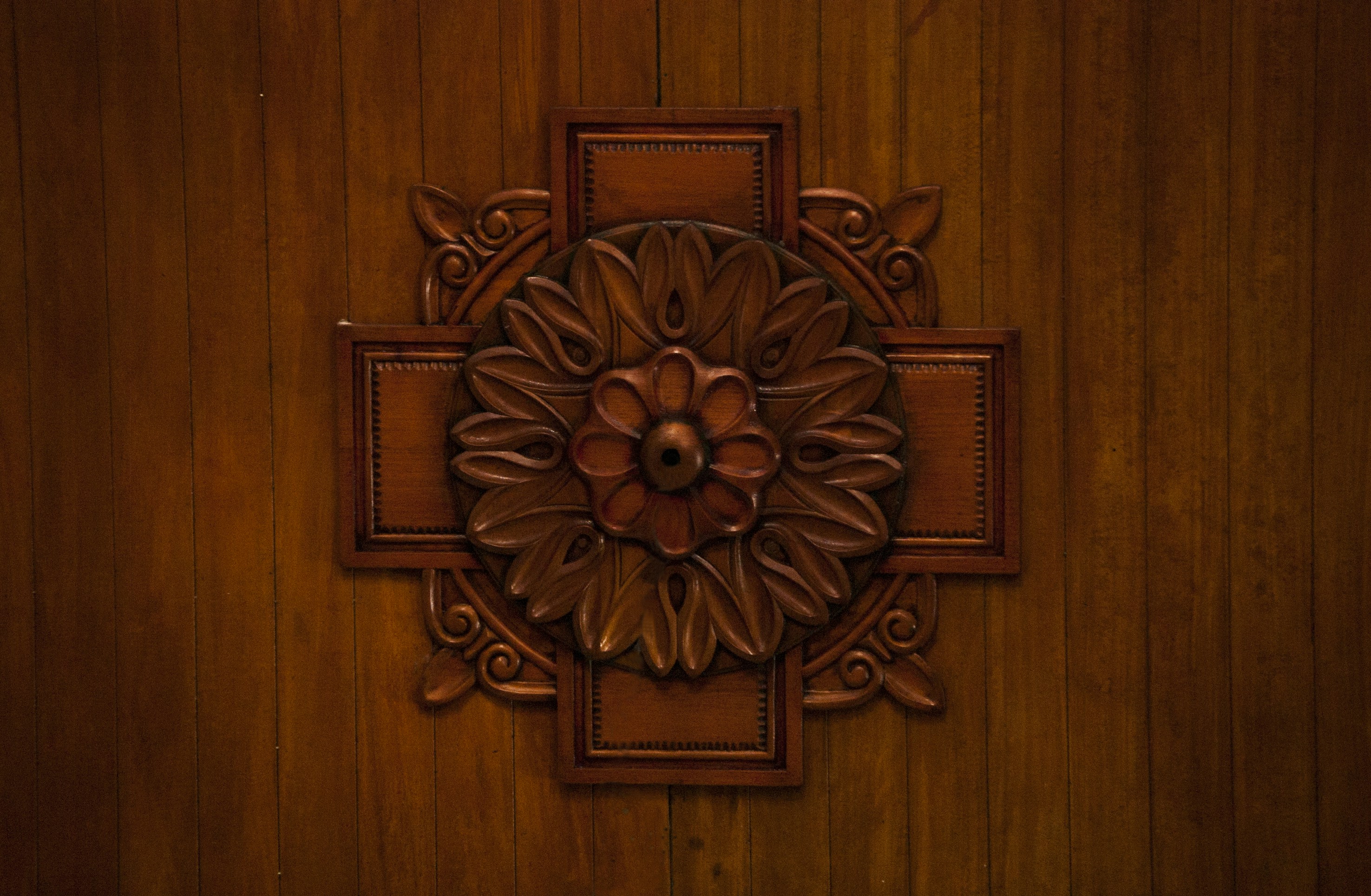 Intricately carved wooden emblem featuring a floral design, centered against a warm wooden backdrop.